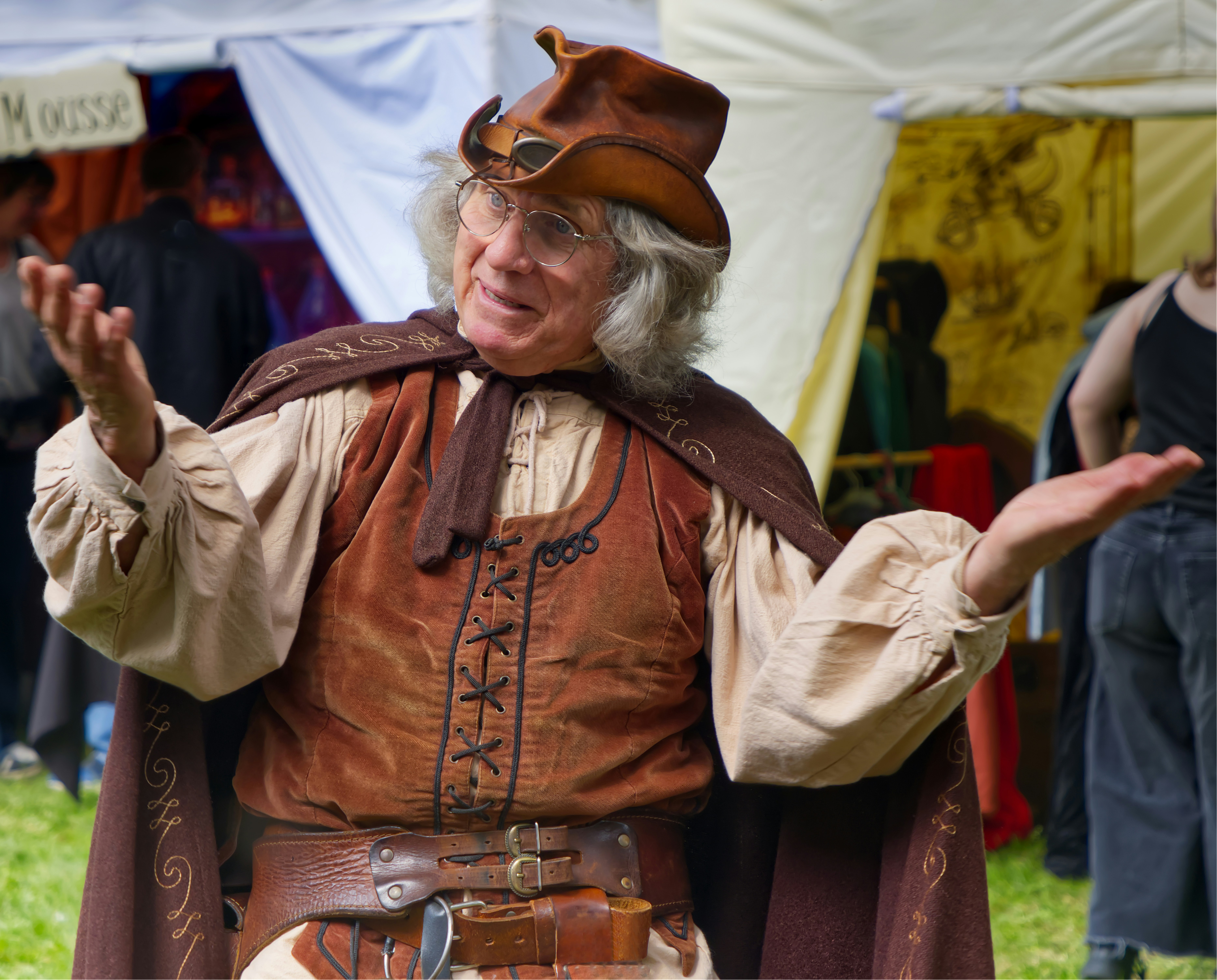 Magnifique portrait d’un vendeur de foire médiévale Il est un gardien de secrets, un conteur d'histoires, un passeur de rêves. Dans ce monde, il est le lien entre le passé et le présent, un guide à travers les méandres du temps et de l'imagination. | A man in medieval costume is talking.