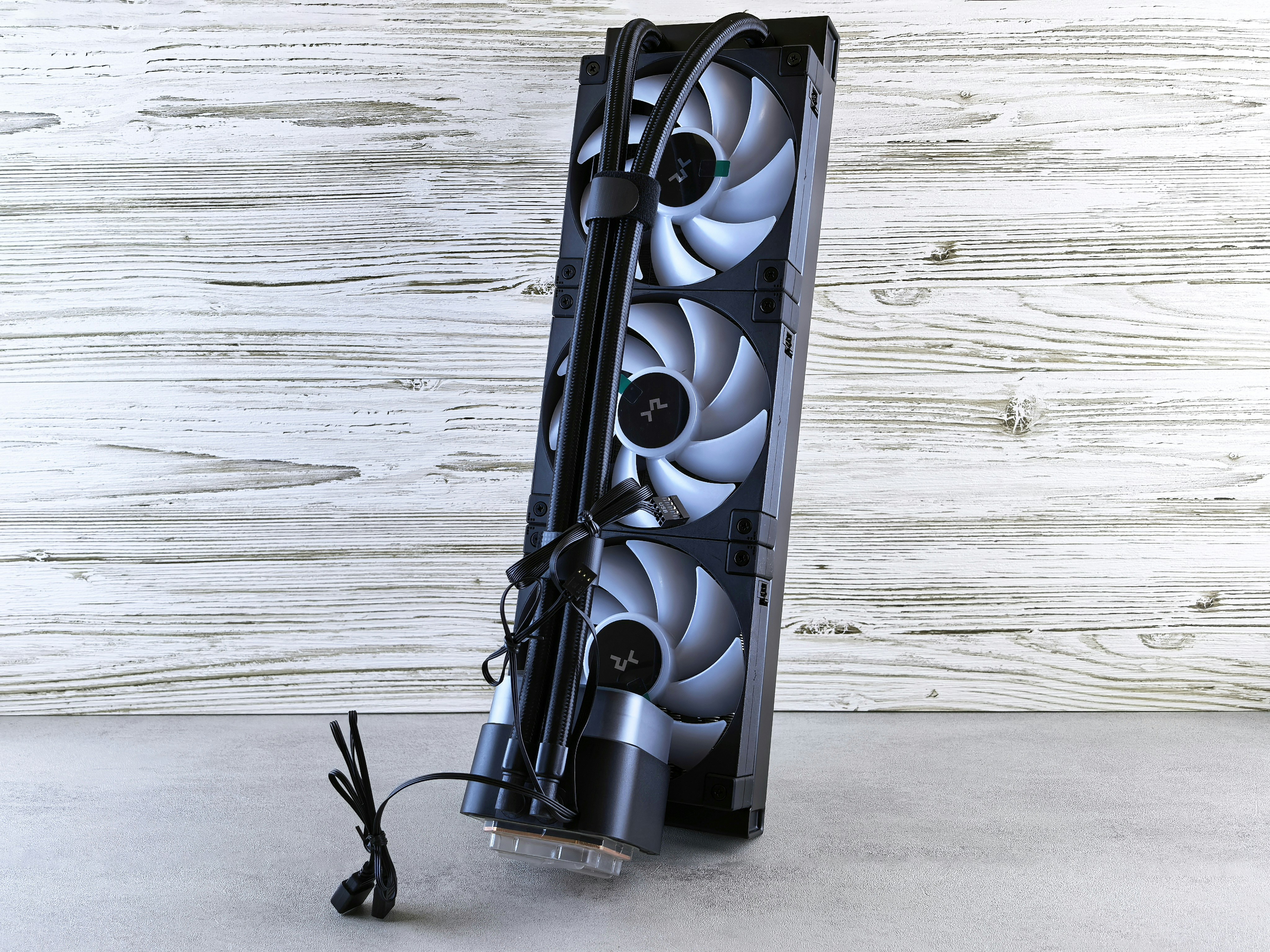 A triple-fan graphics card rests upright on a light wooden surface, with cables draped along its side.