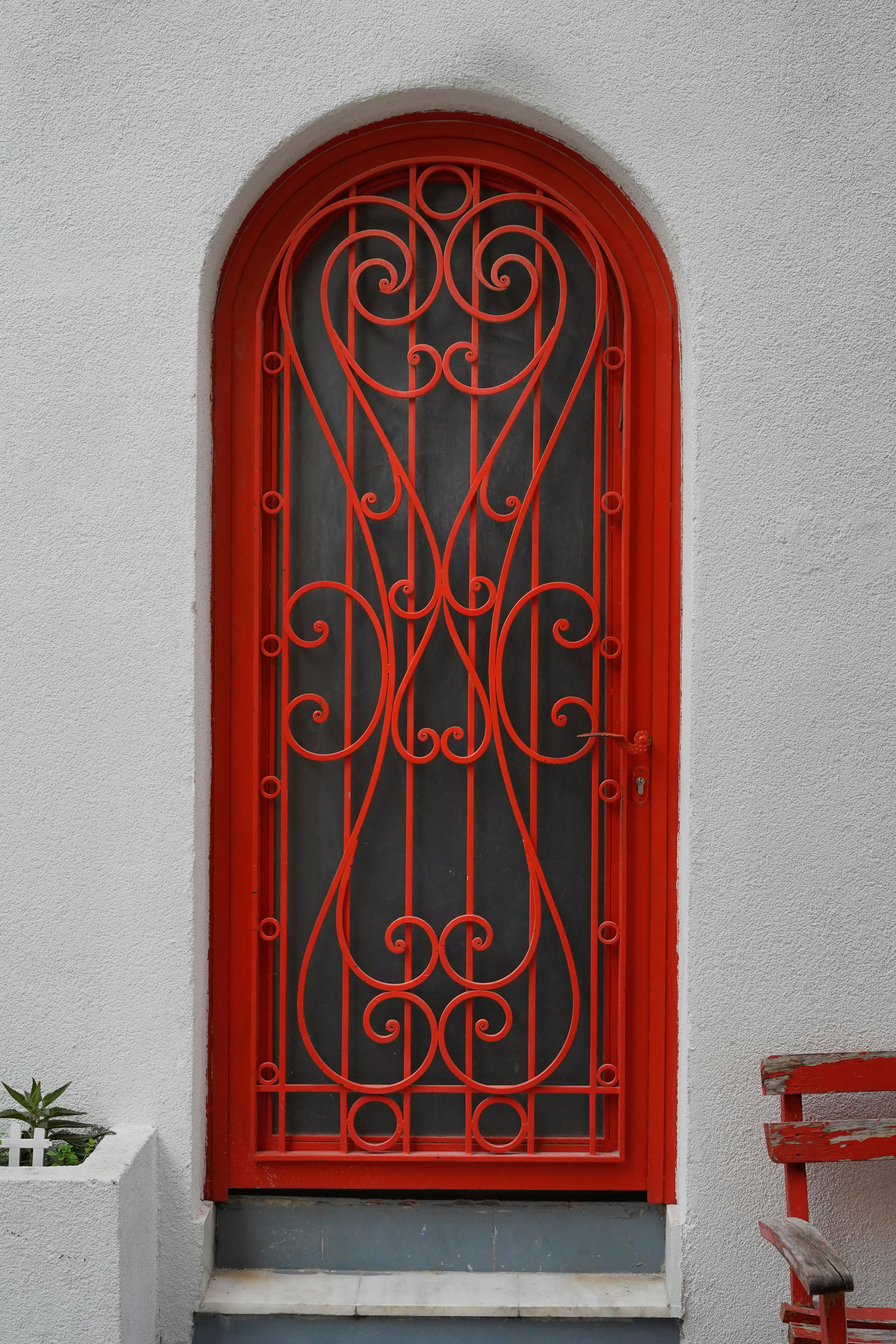 Crimson Arch Gate with Ornate Ironwork on a Pale Facade