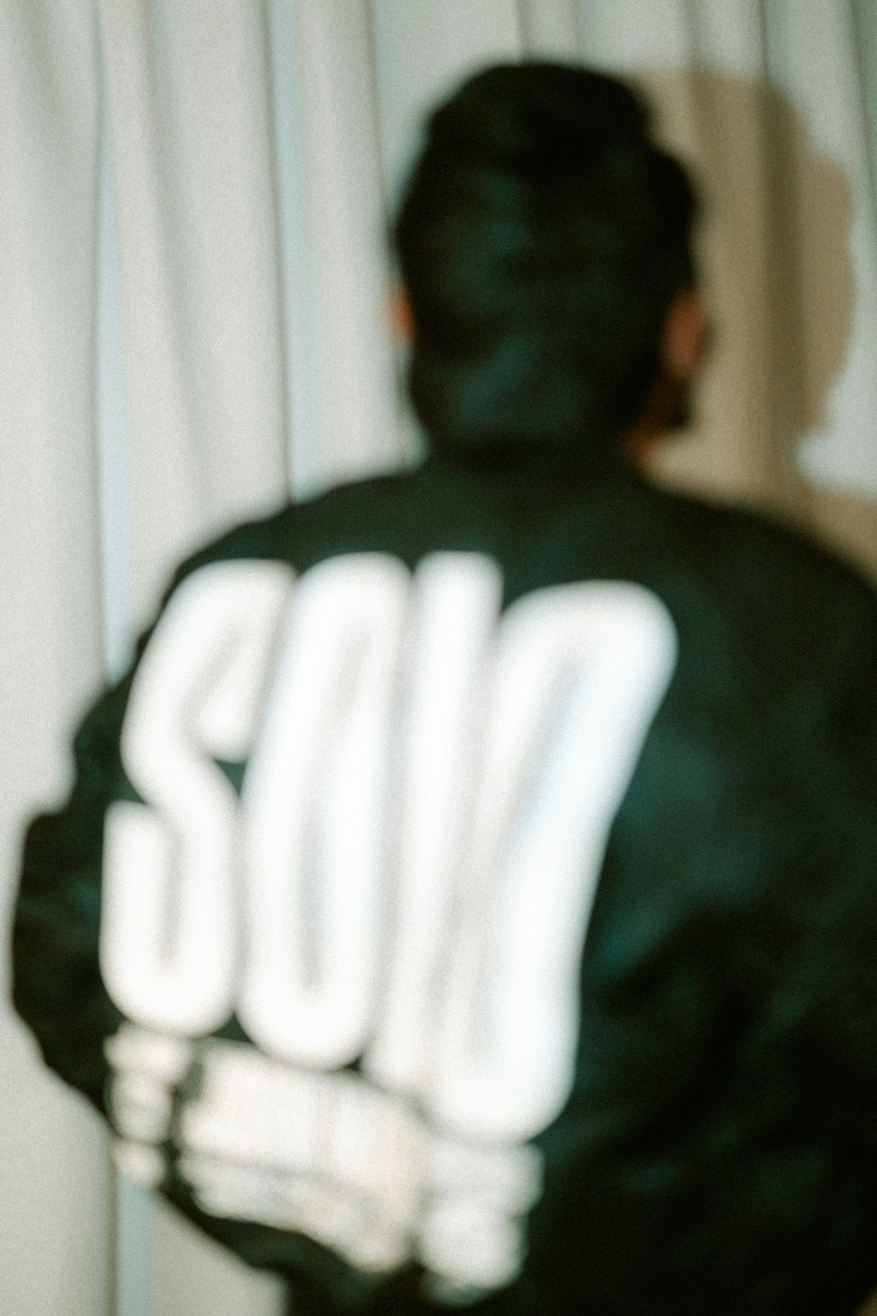 A figure in a black jacket with the word 'SOLO' stands against a softly draped curtain, evoking a sense of introspection.
