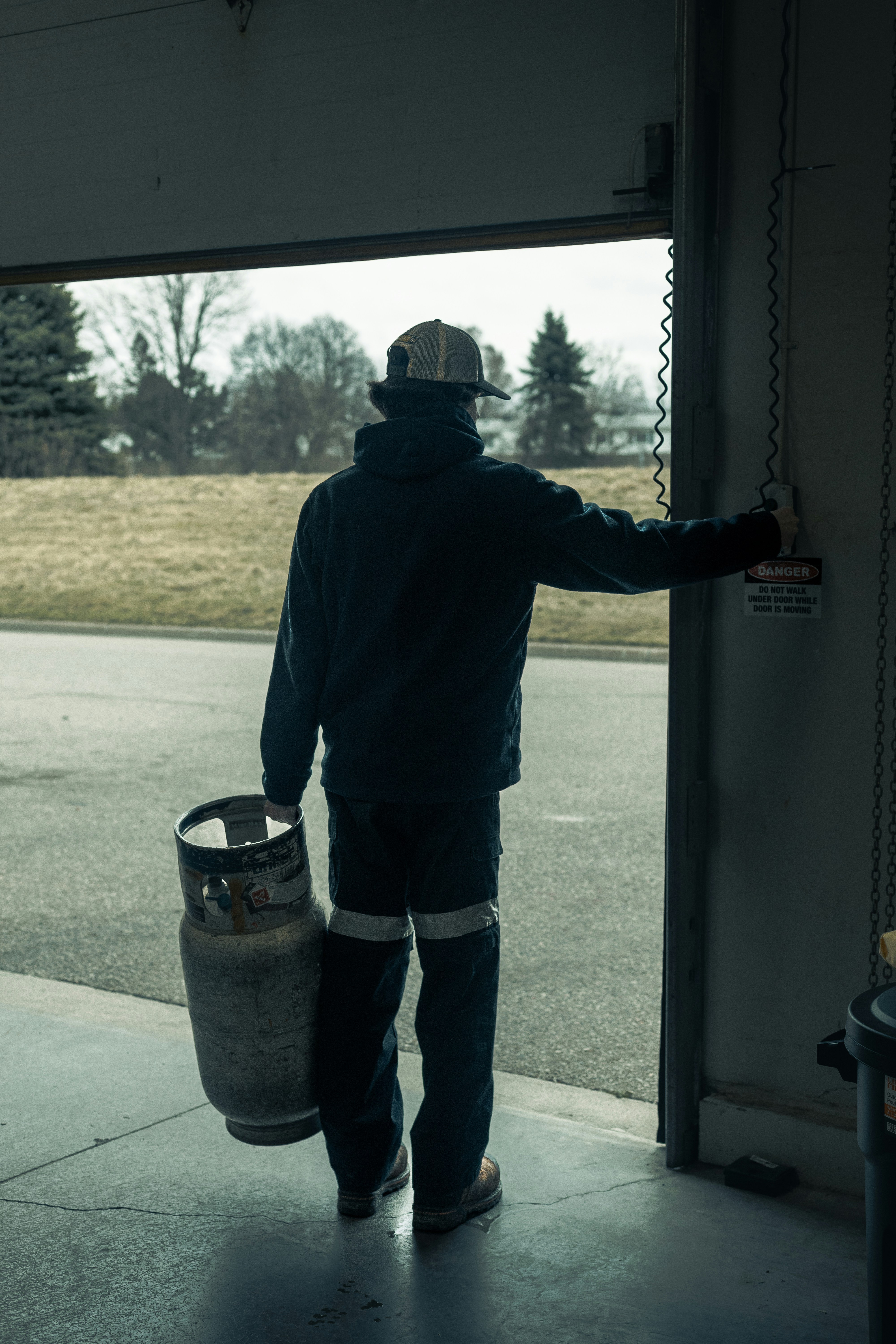Propane Pause: A Helmed Worker Steps Out from the Garage