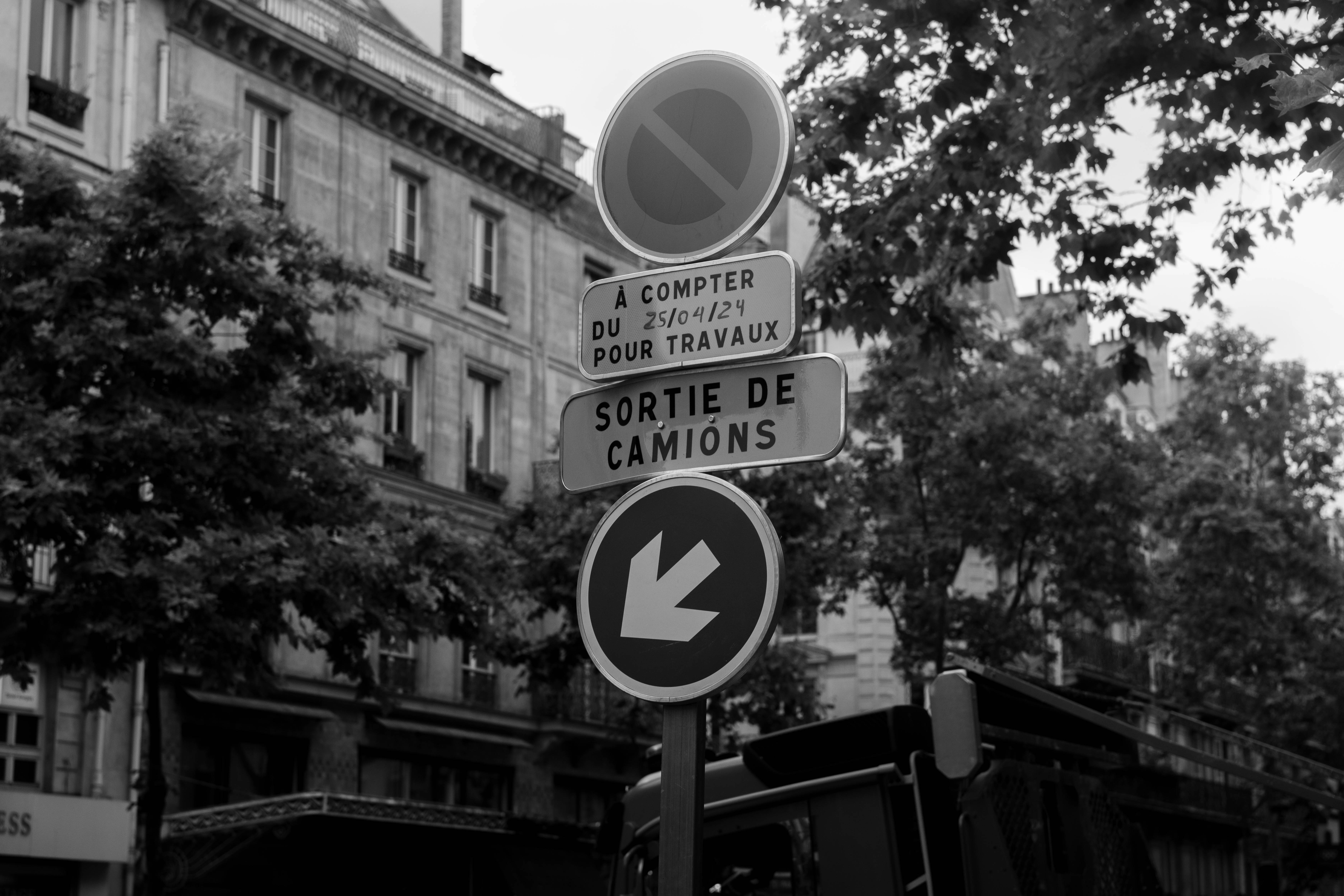 Traffic signs indicating construction work and truck exit in a bustling city environment.