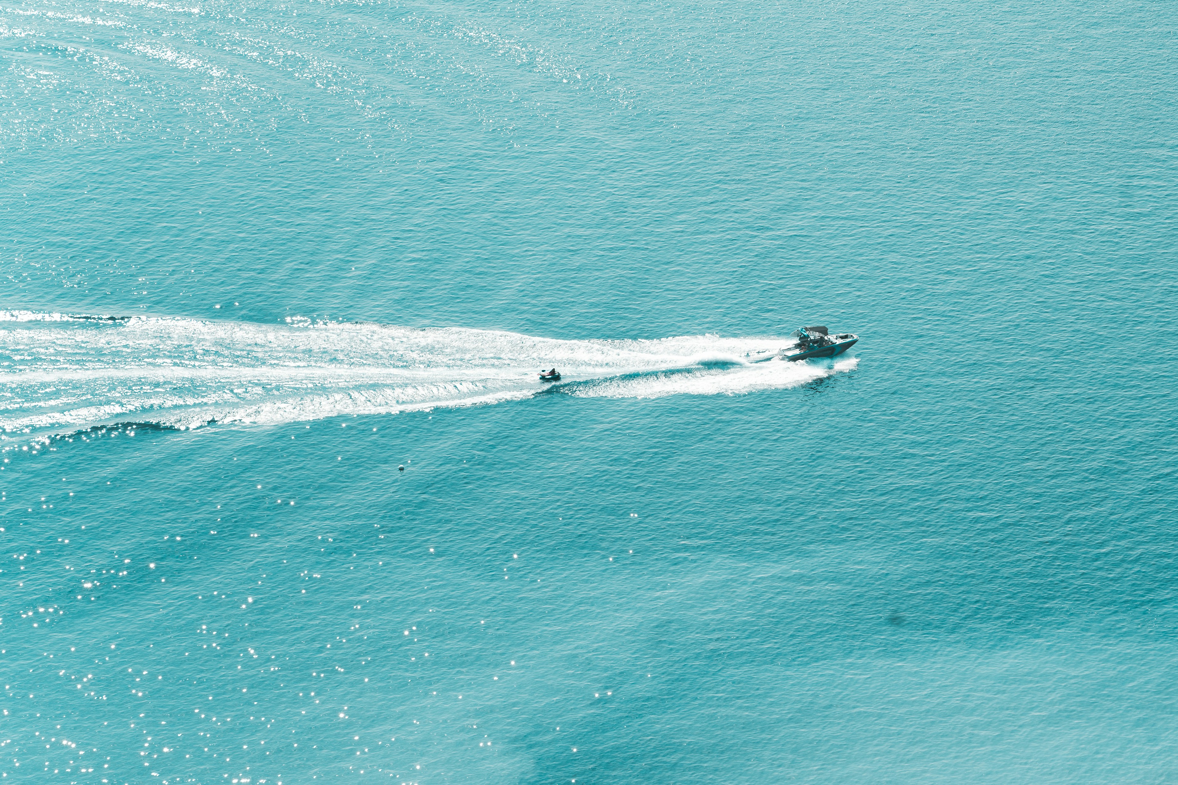 Two boats glide across a tranquil turquoise sea, leaving shimmering trails in their wake.
