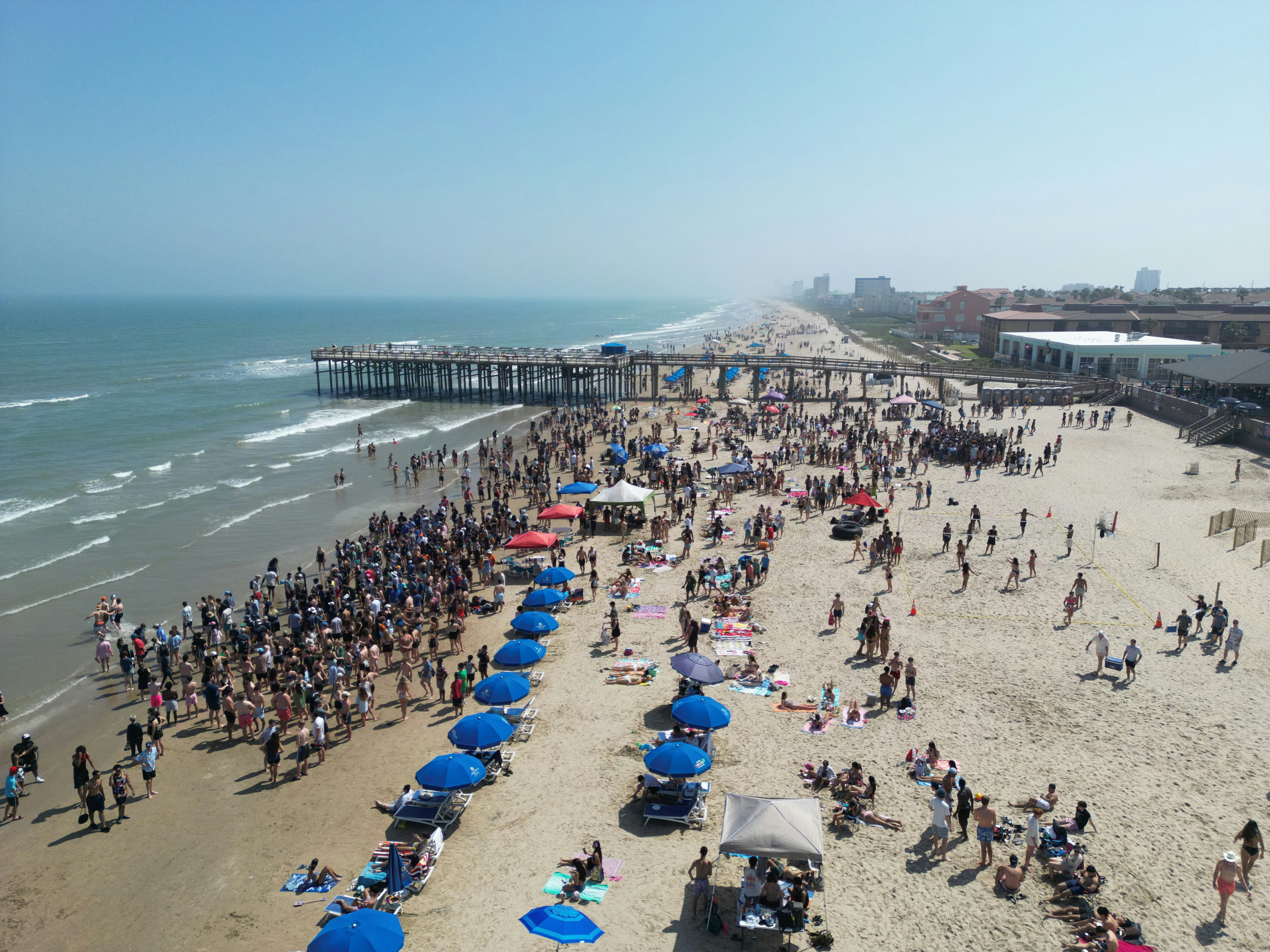 Bustling Beachfront: A Long Pier Framing a Sea of Blue Umbrellas