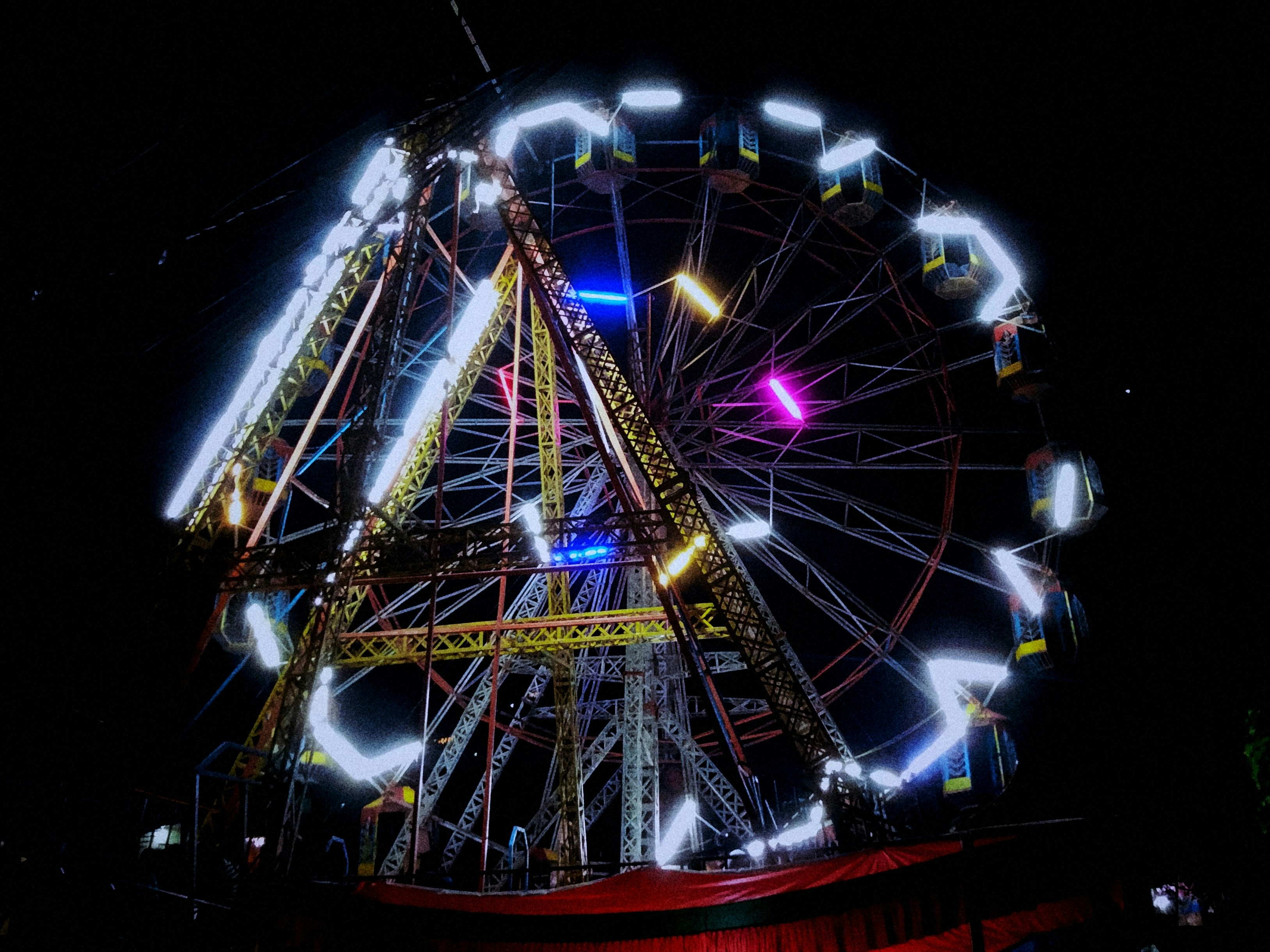 Vibrant ferris wheel adorned with colorful lights spinning against the night sky, creating a festive atmosphere.