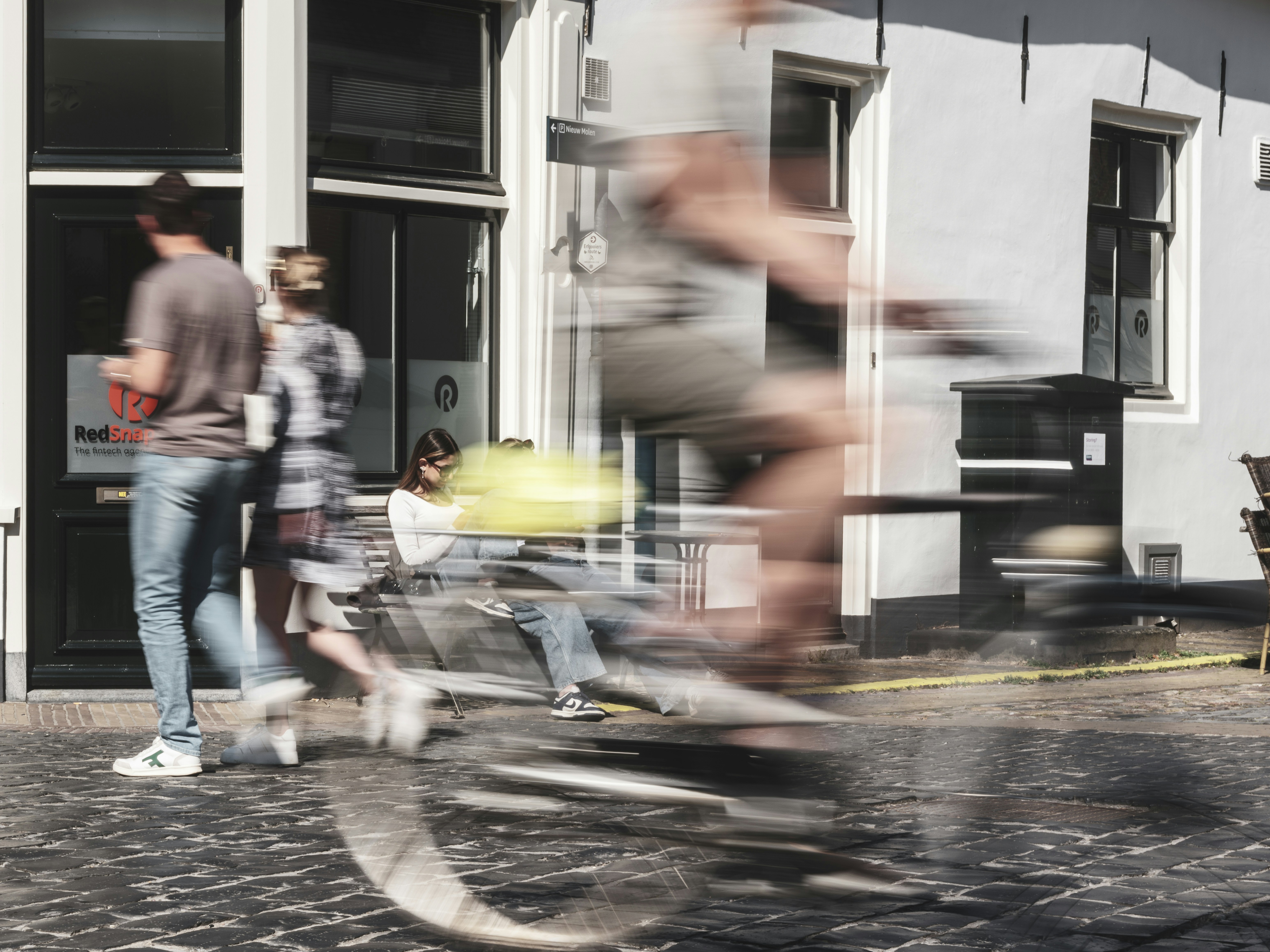 Stillness on a Blurred Boulevard: A Seated Figure Amid Transit Motion
