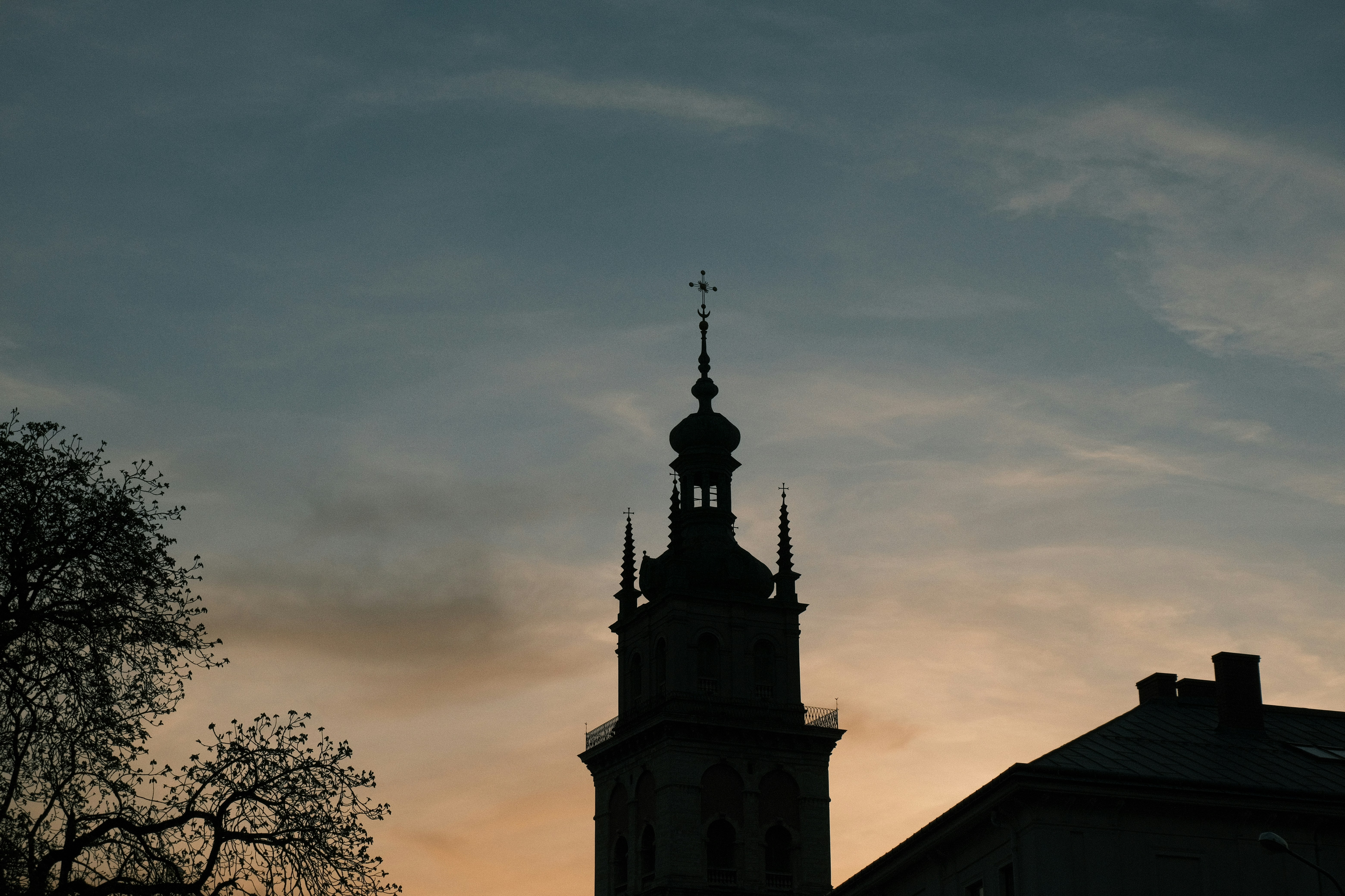 Historic tower silhouetted against a colorful twilight sky, framed by the branches of a nearby tree.