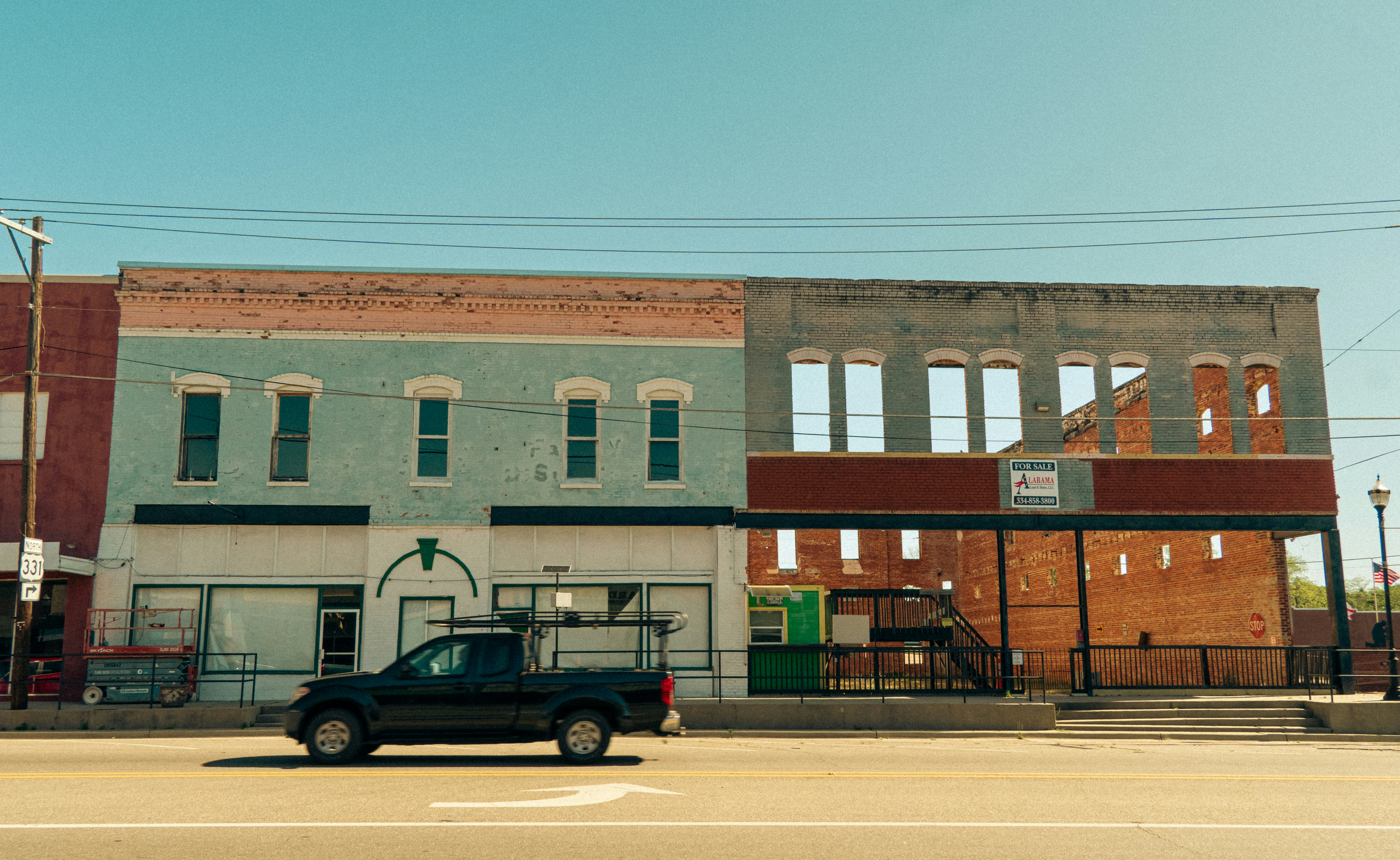 Abandoned buildings with faded facades and a passing black truck under a clear sky.