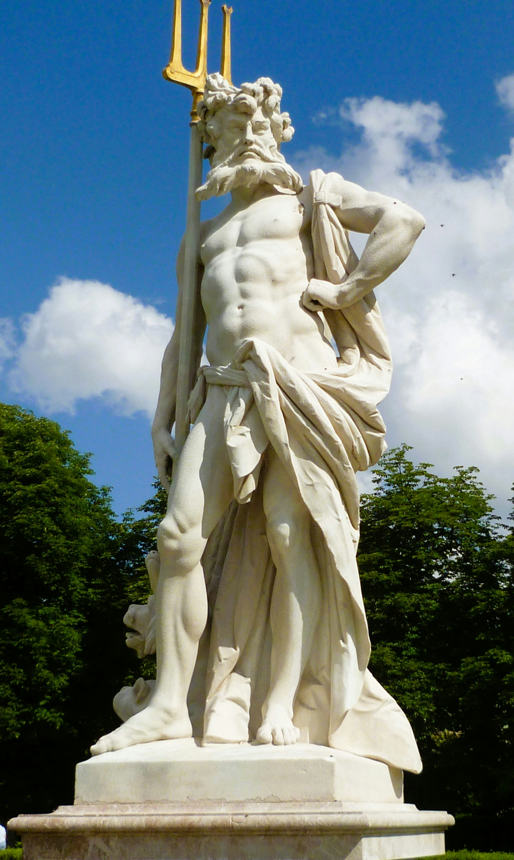 A majestic statue of a sea god, adorned with a trident, standing confidently amidst lush greenery and a bright blue sky.