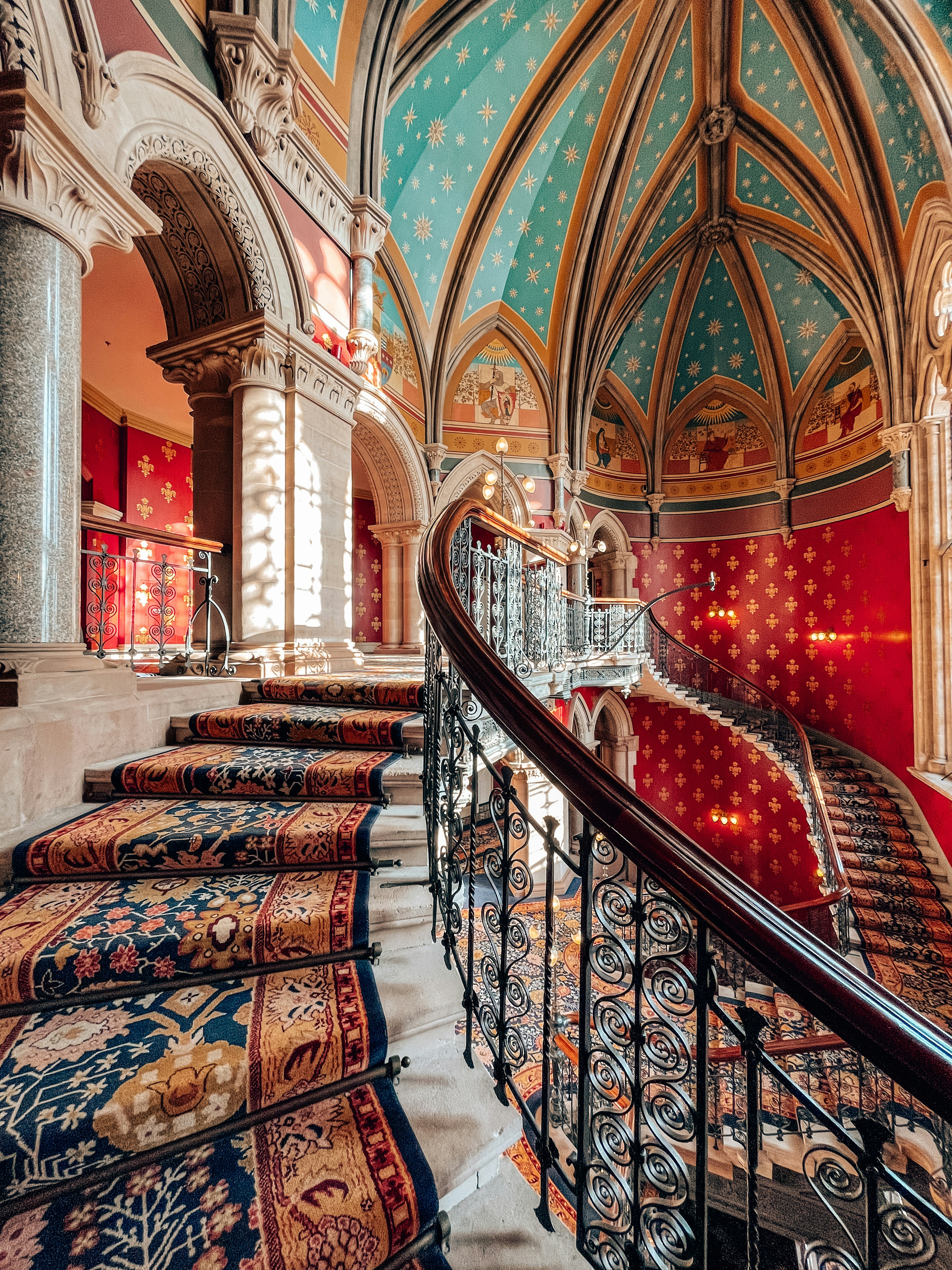 Intricate staircase adorned with ornate carpets, leading to a beautifully painted ceiling in a grand hall.