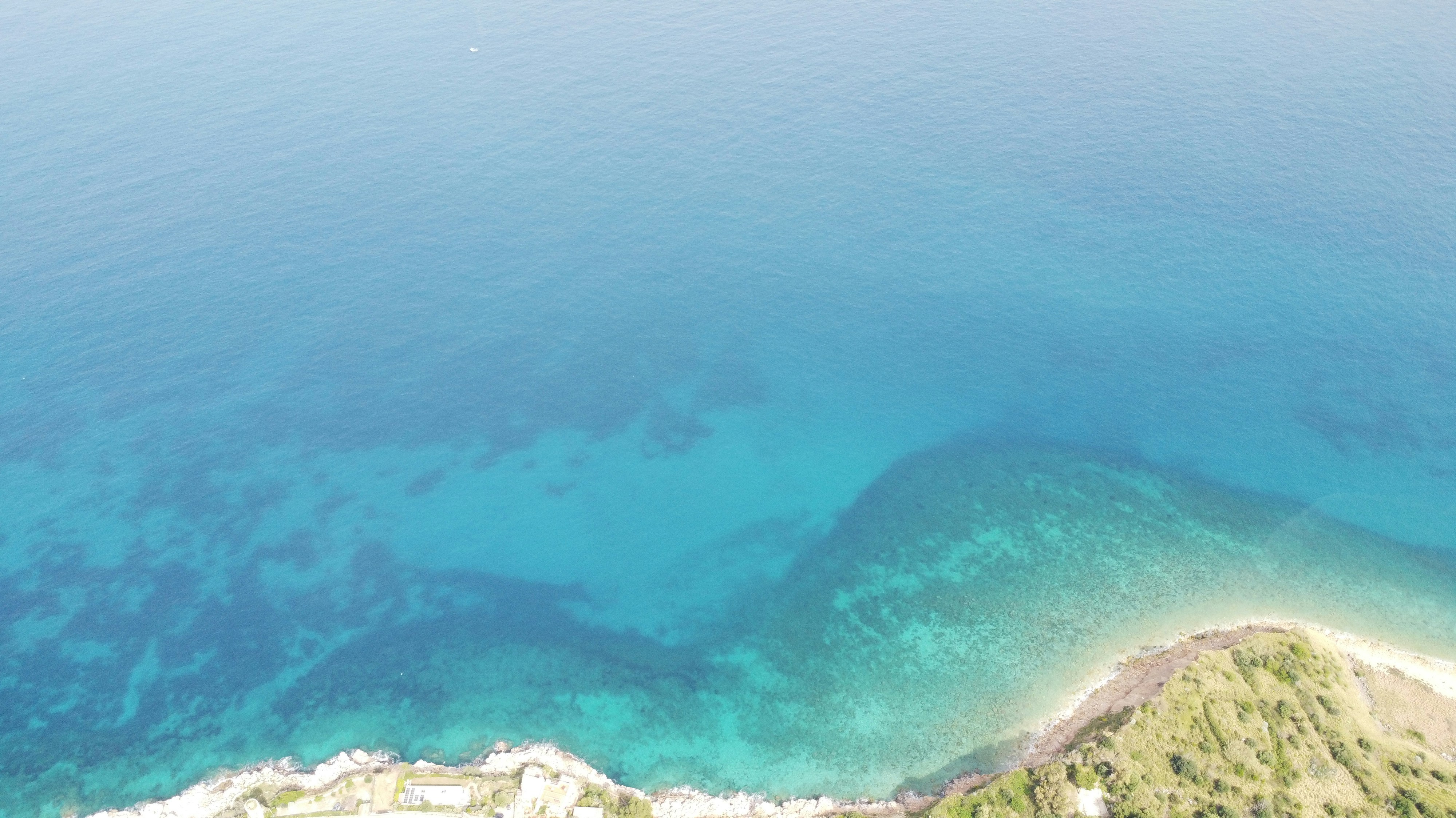 Aerial view of turquoise shallows meeting a grassy headland along a rugged coastline.