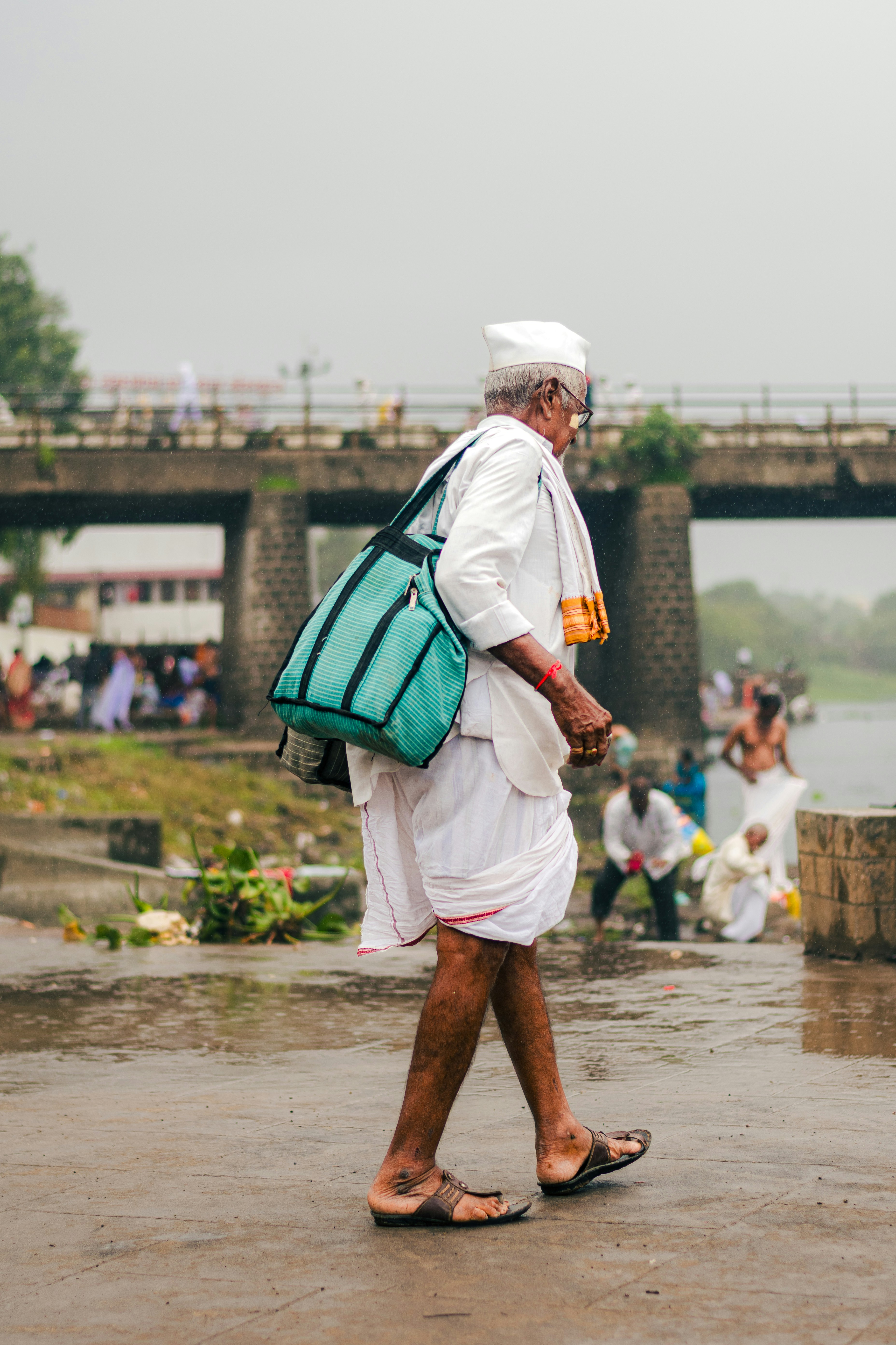 An elderly man walks near a river.