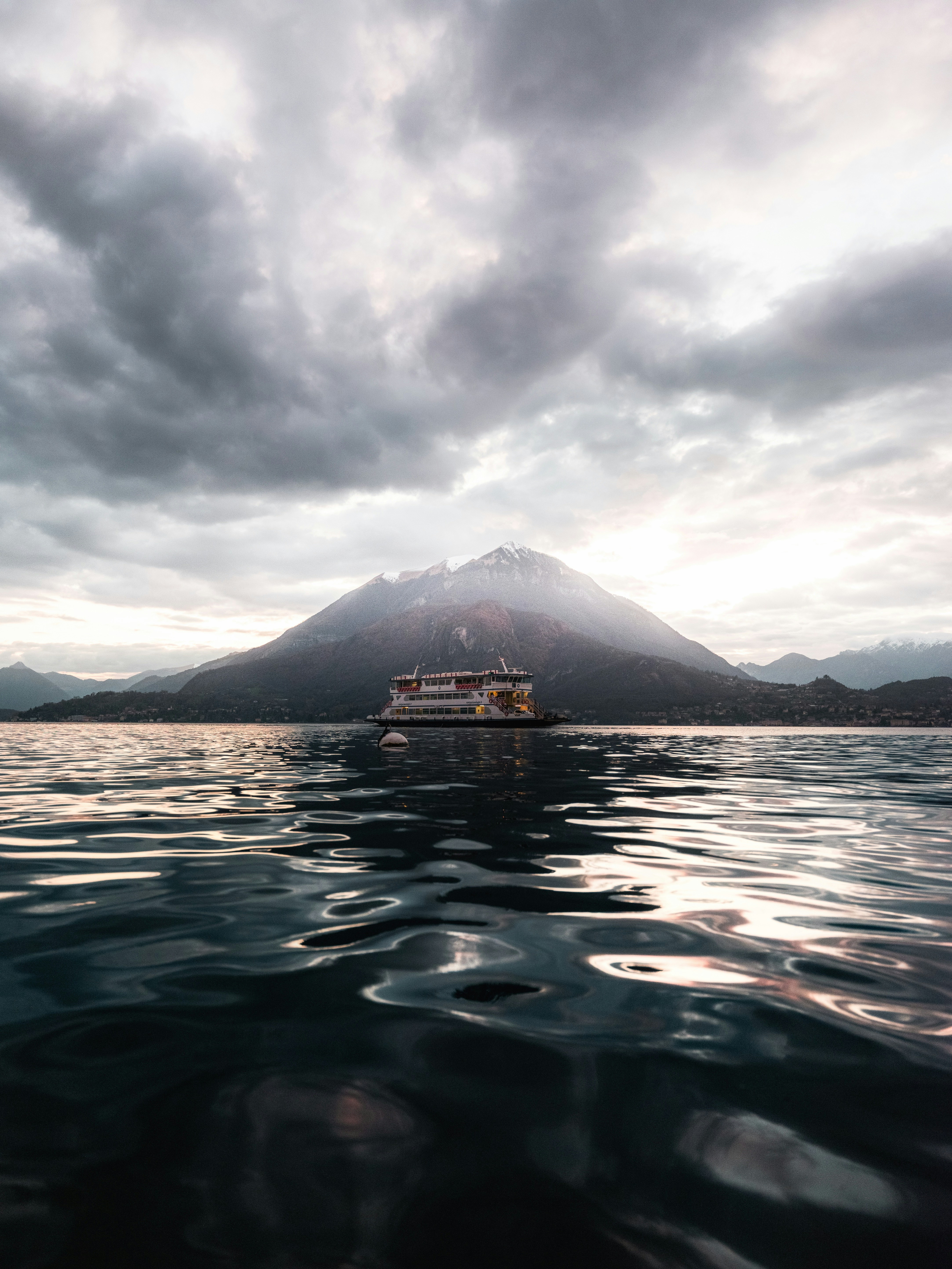 Un bote flota en el lago bajo una montaña nublada. foto – Imagen de ...