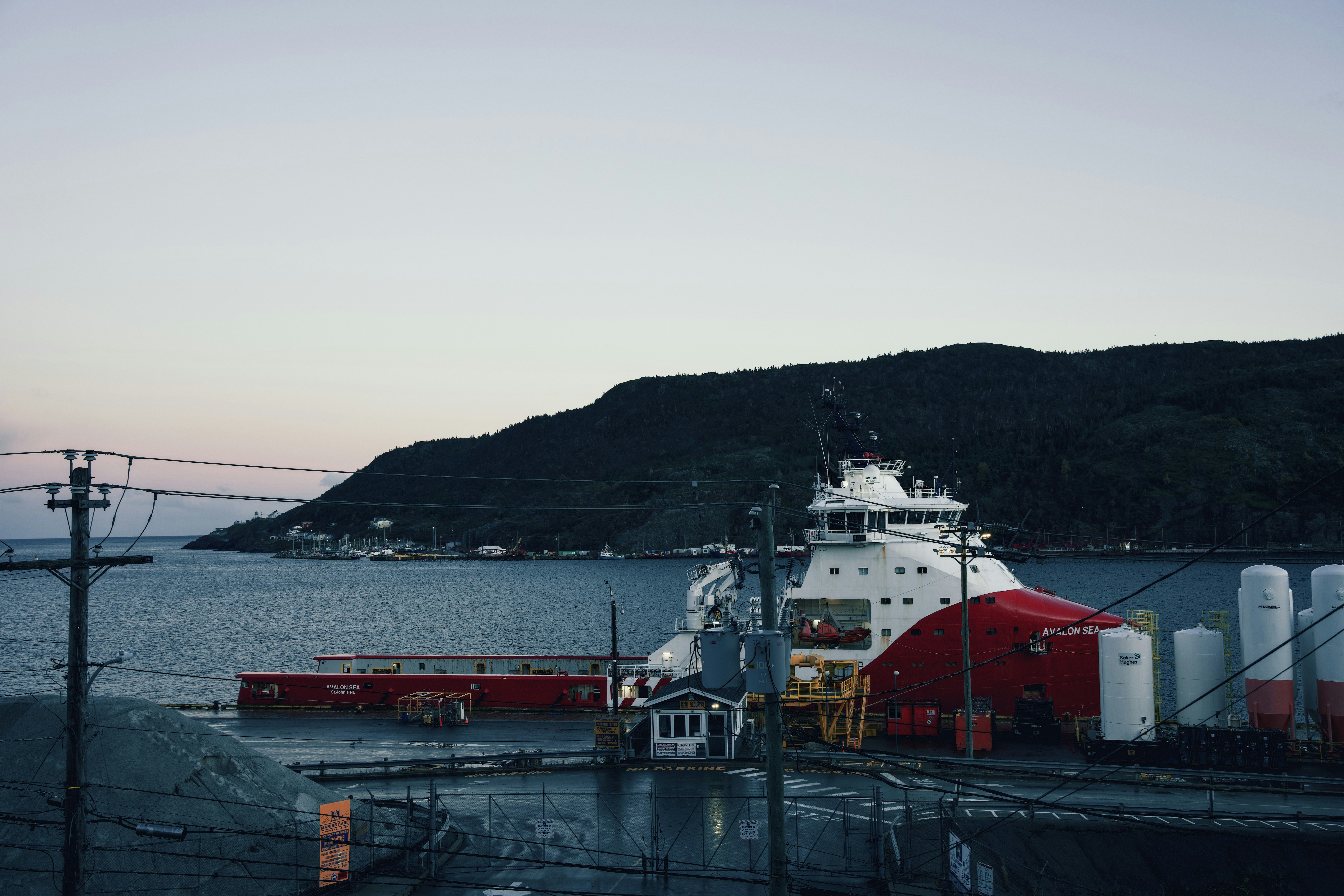 Red-hulled freighter at twilight harbor beneath the quiet peninsula