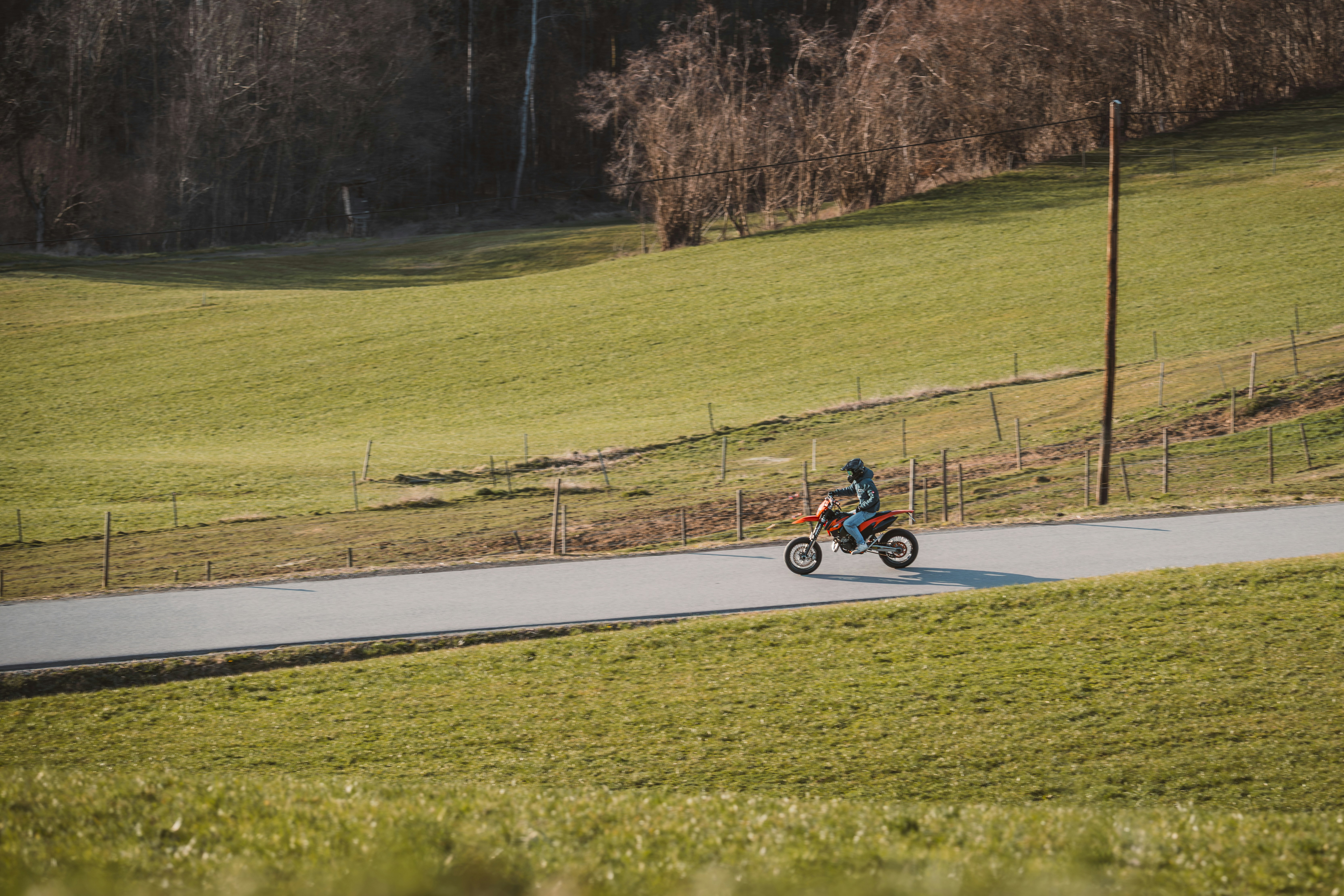 Solitary motorcycle tracer on a sunlit rural road through rolling meadows