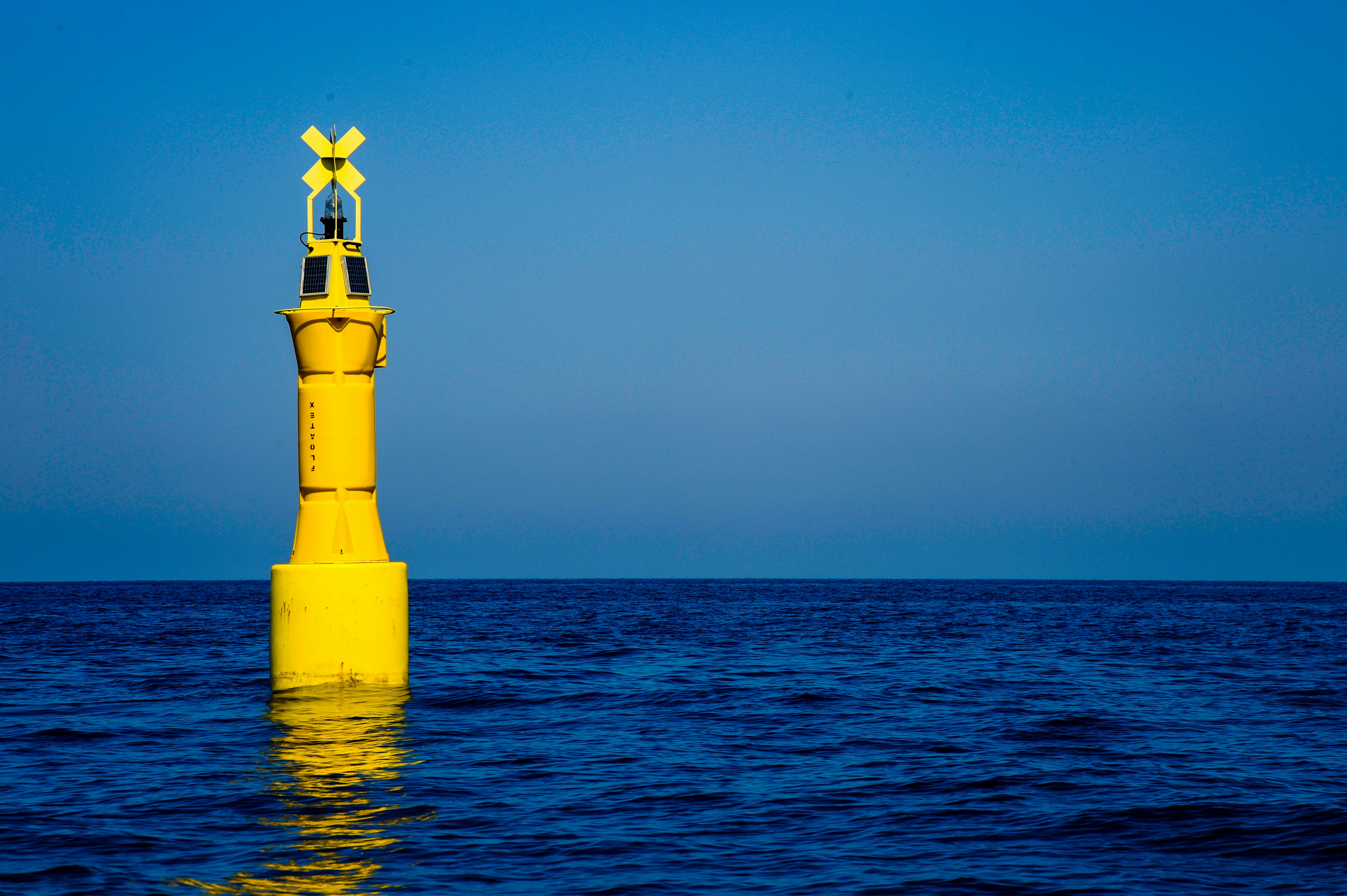Lone yellow buoy punctuates cobalt sea under a clear sky