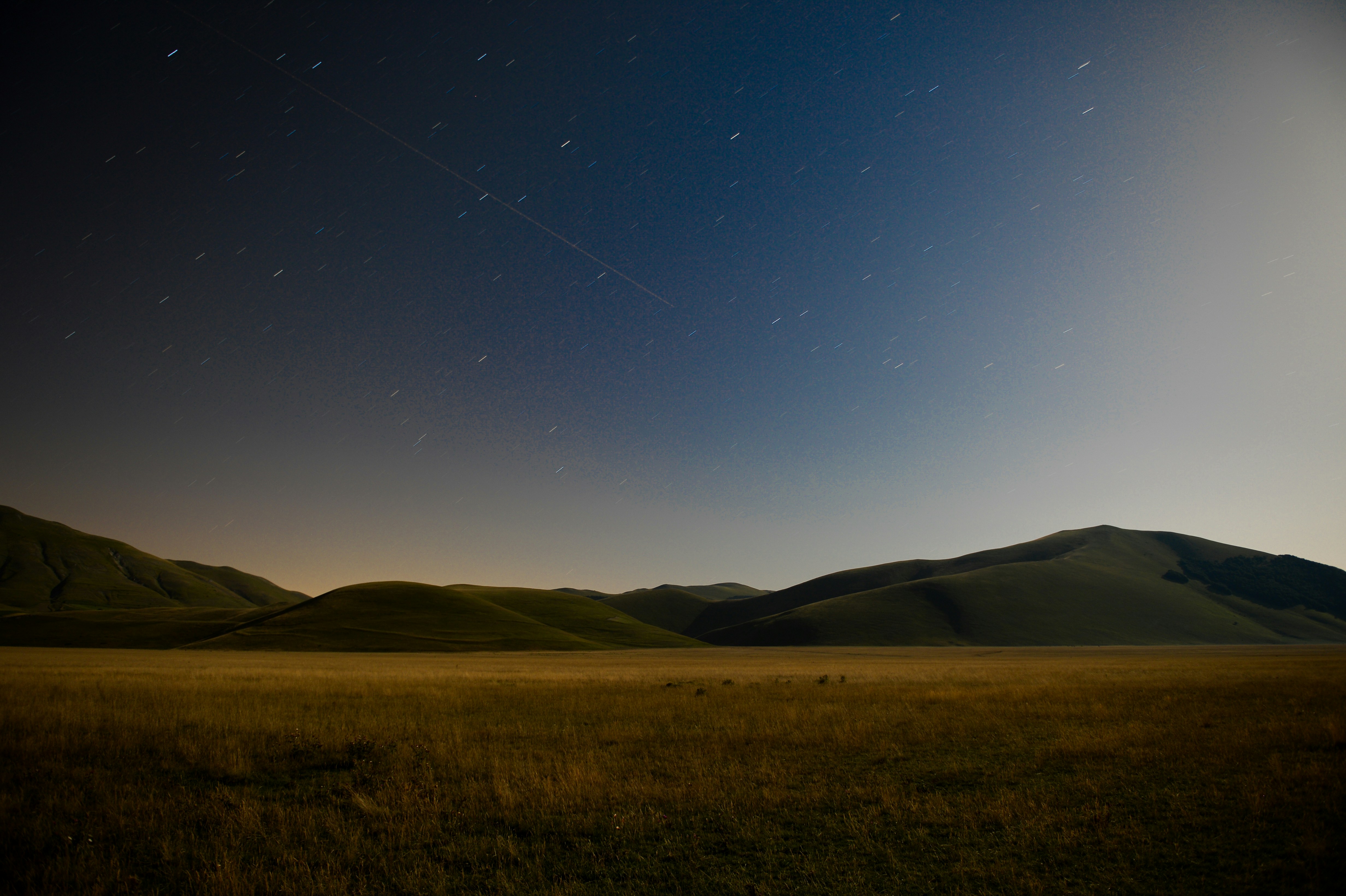 Stars shine above a grassy field and mountains. photo – Free Wallpaper ...