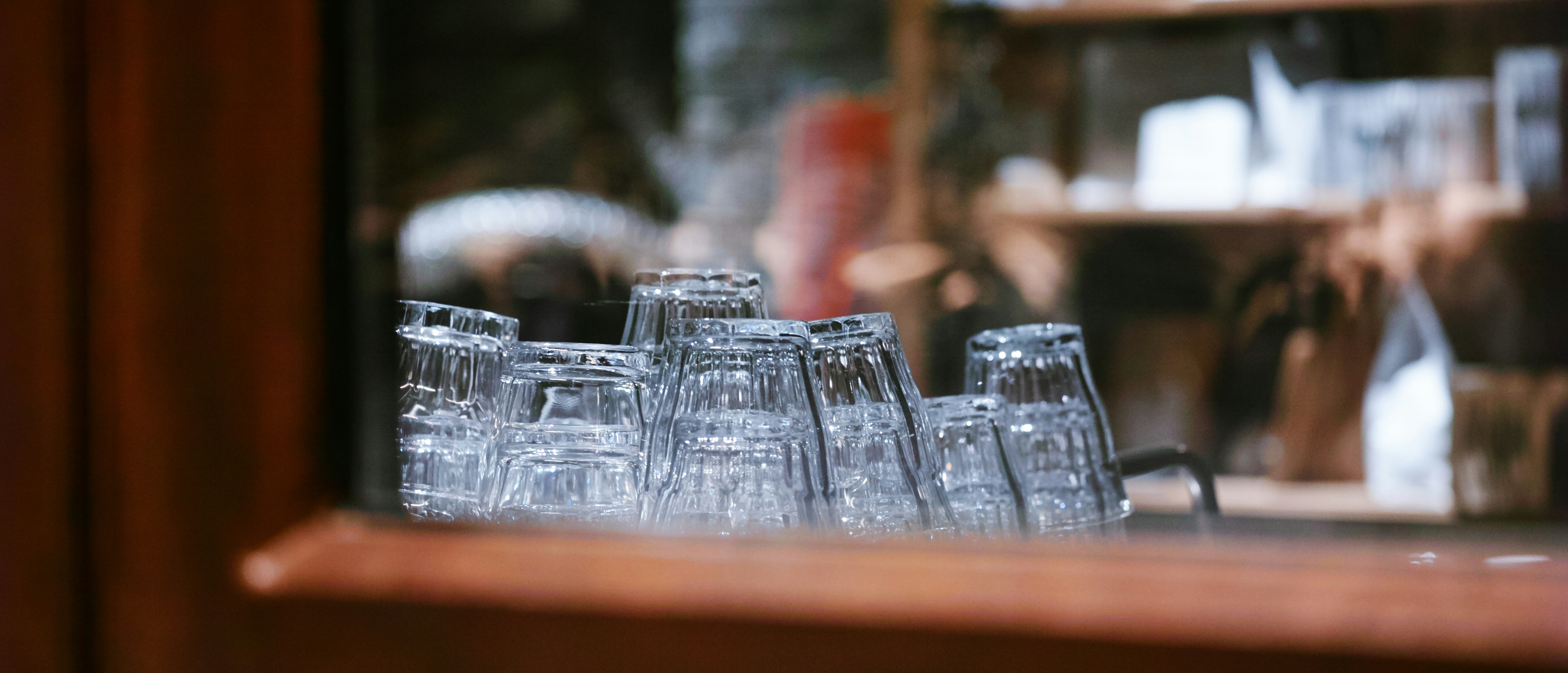 Stacked glassware viewed through a wooden frame, hinting at a cozy interior setting. The arrangement suggests a moment of anticipation in a bustling café.