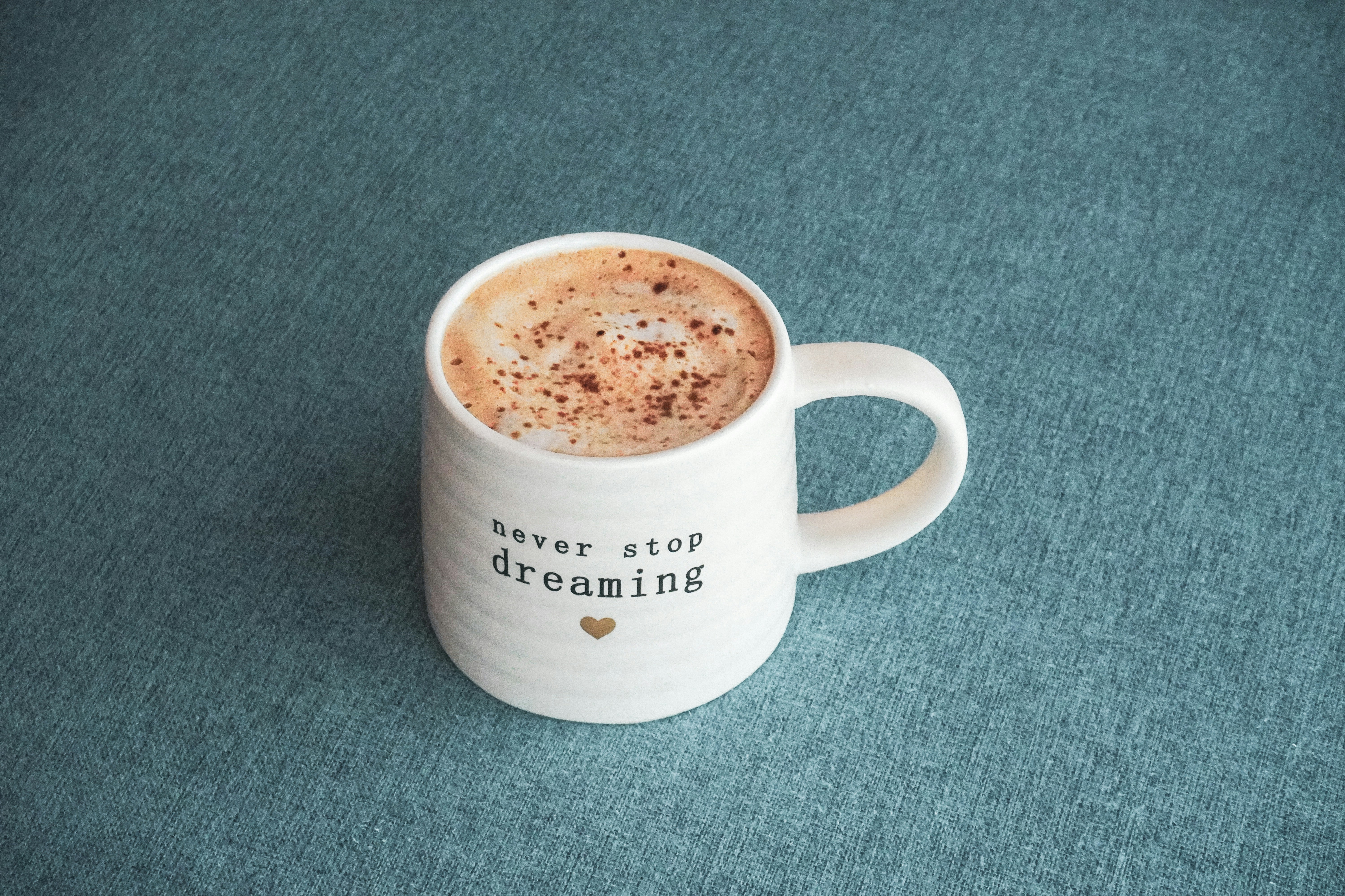 Never Stop Dreaming: A White Ceramic Mug on Textured Teal Linen