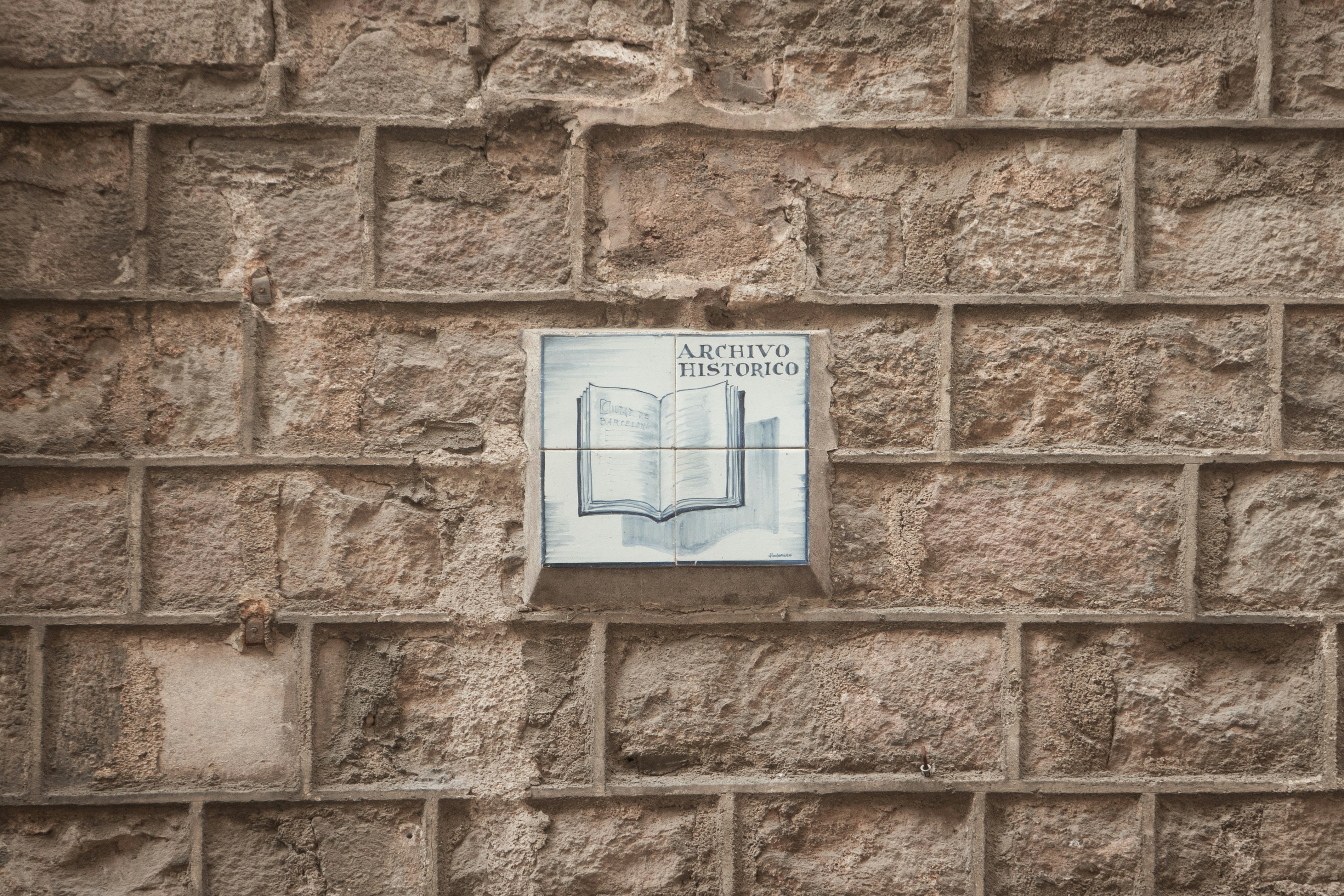 A tile displays a book on a brick wall. photo – Free Building Image on ...