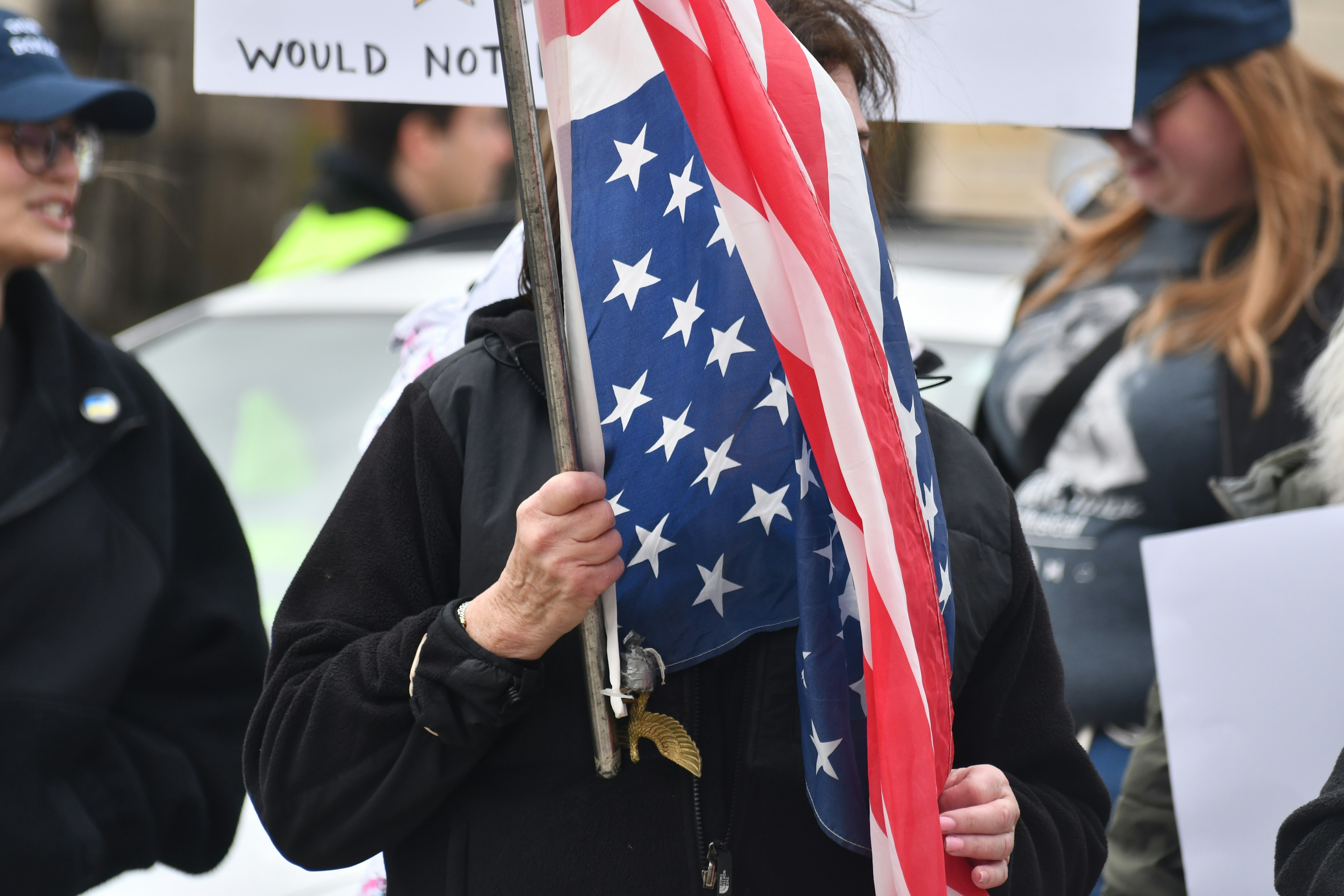 Crimson Stripes, Quiet Resolve: A Flag Framed by Protest Signs