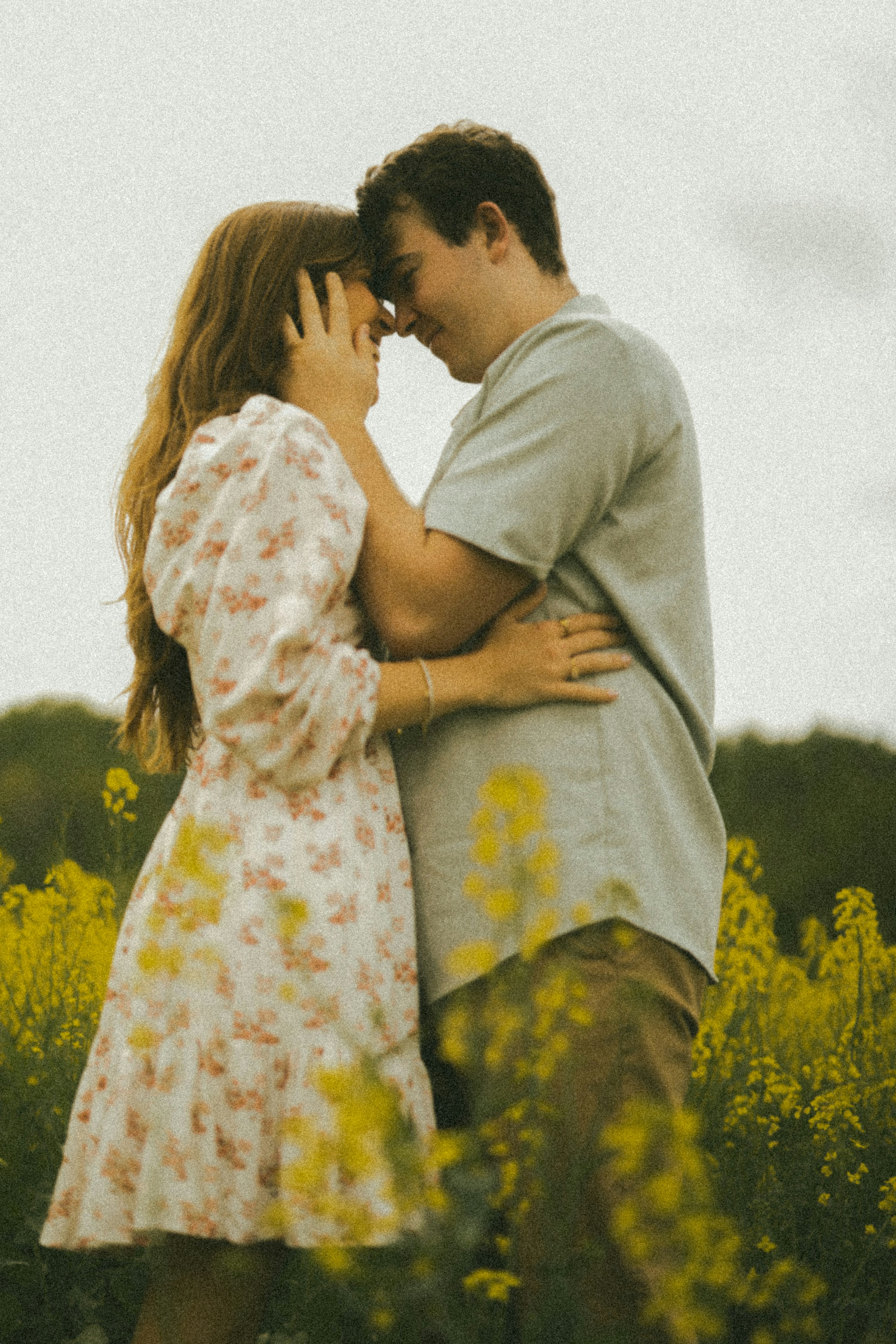 Couple embracing in a field of wildflowers, sharing an intimate moment as they lean in close. Soft, dreamy atmosphere enhances their connection.