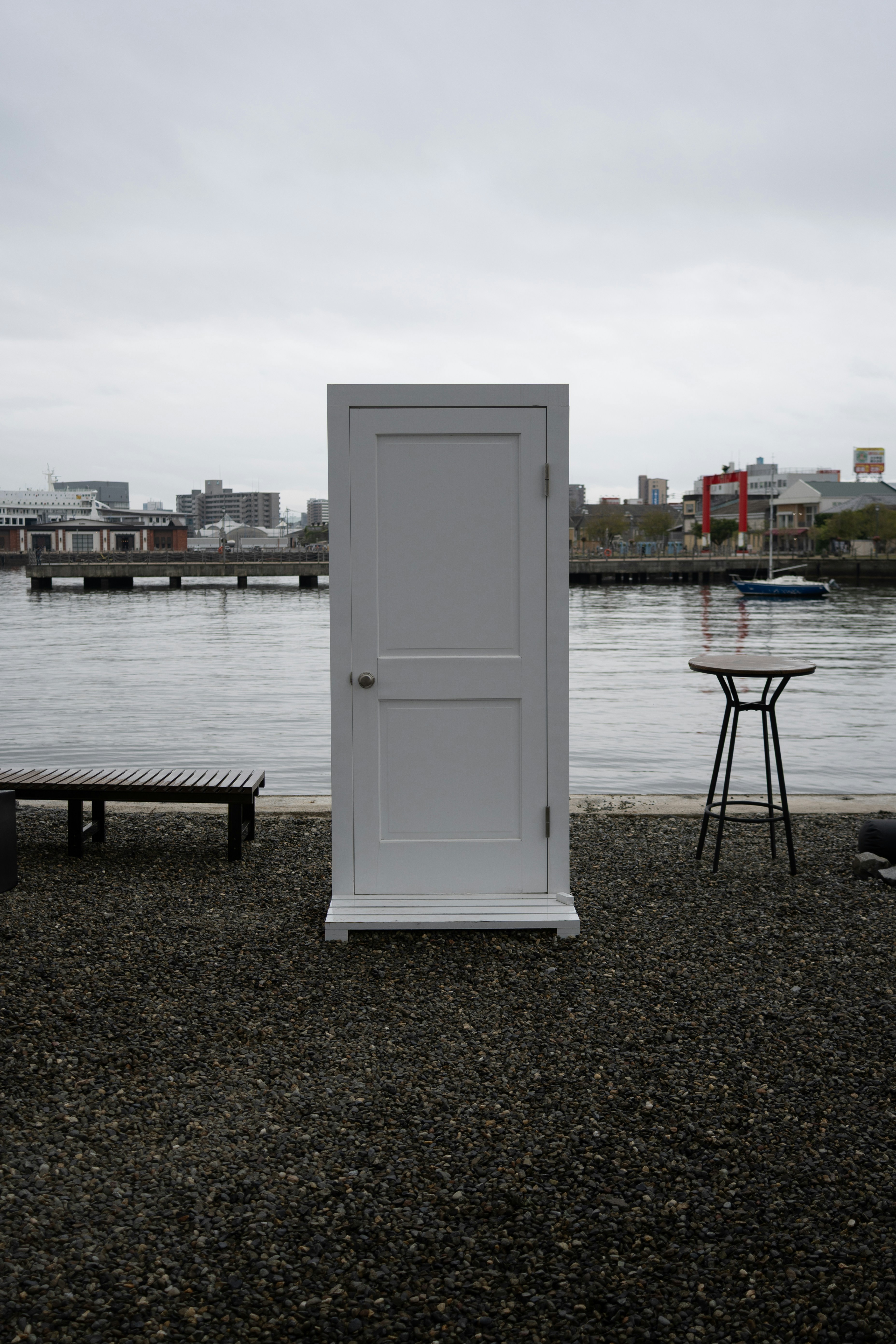 A solitary doorway anchors the harbor: a doorway standing solo on pebbled shore