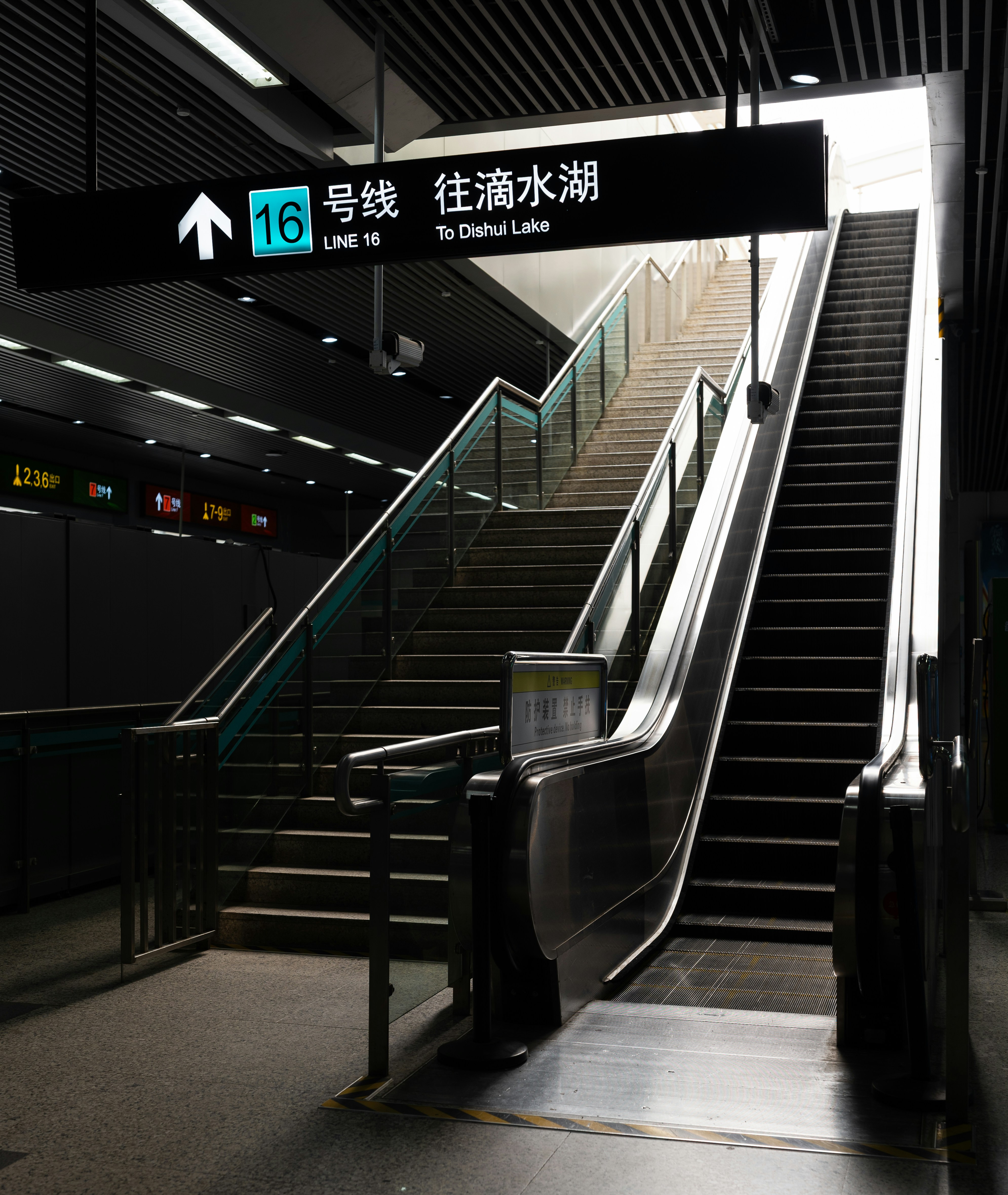 Escalator Ascent Under Neon Signage in Metro Hall