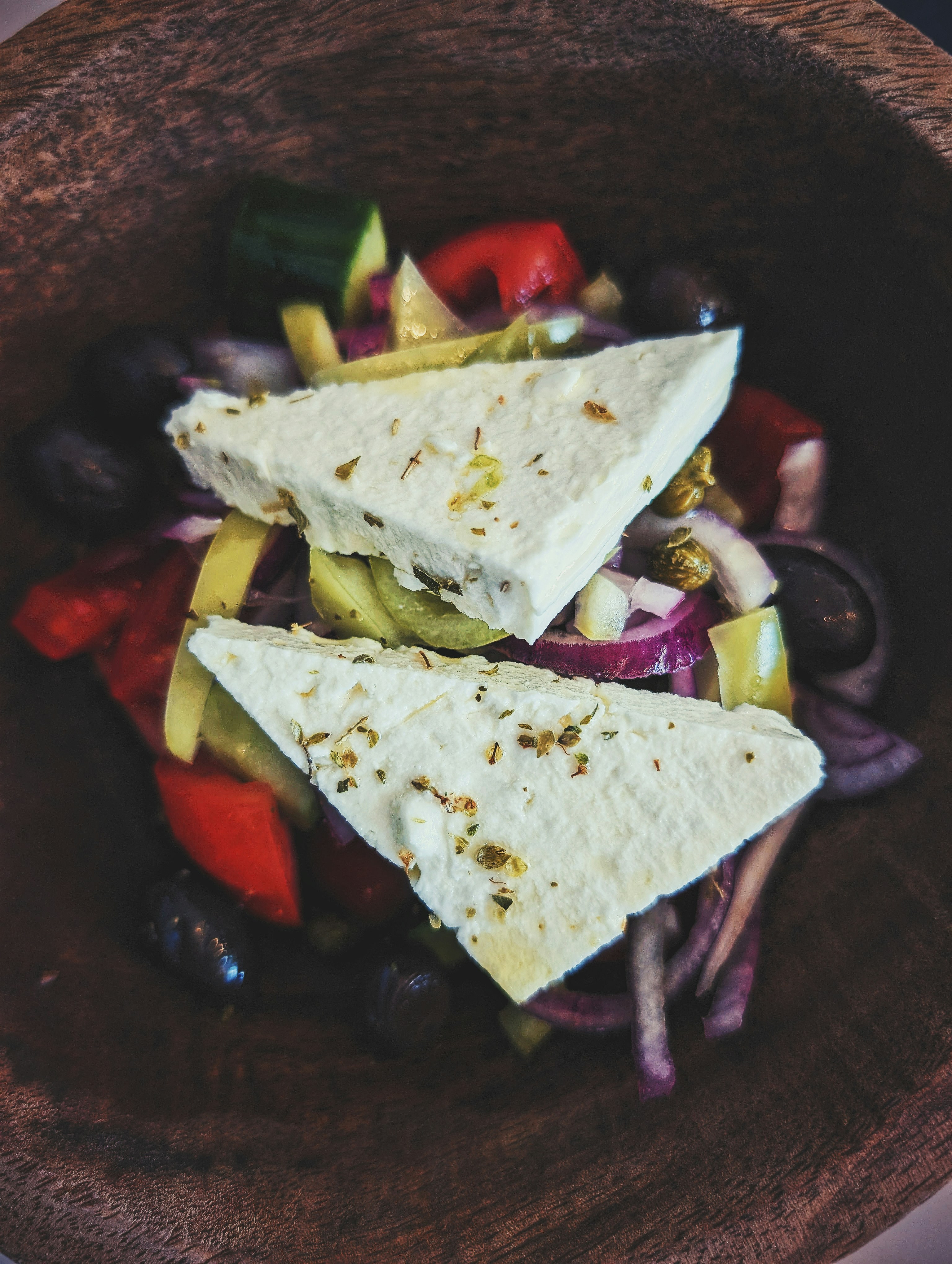 Fresh salad featuring vibrant vegetables topped with feta cheese, served in a rustic wooden bowl.