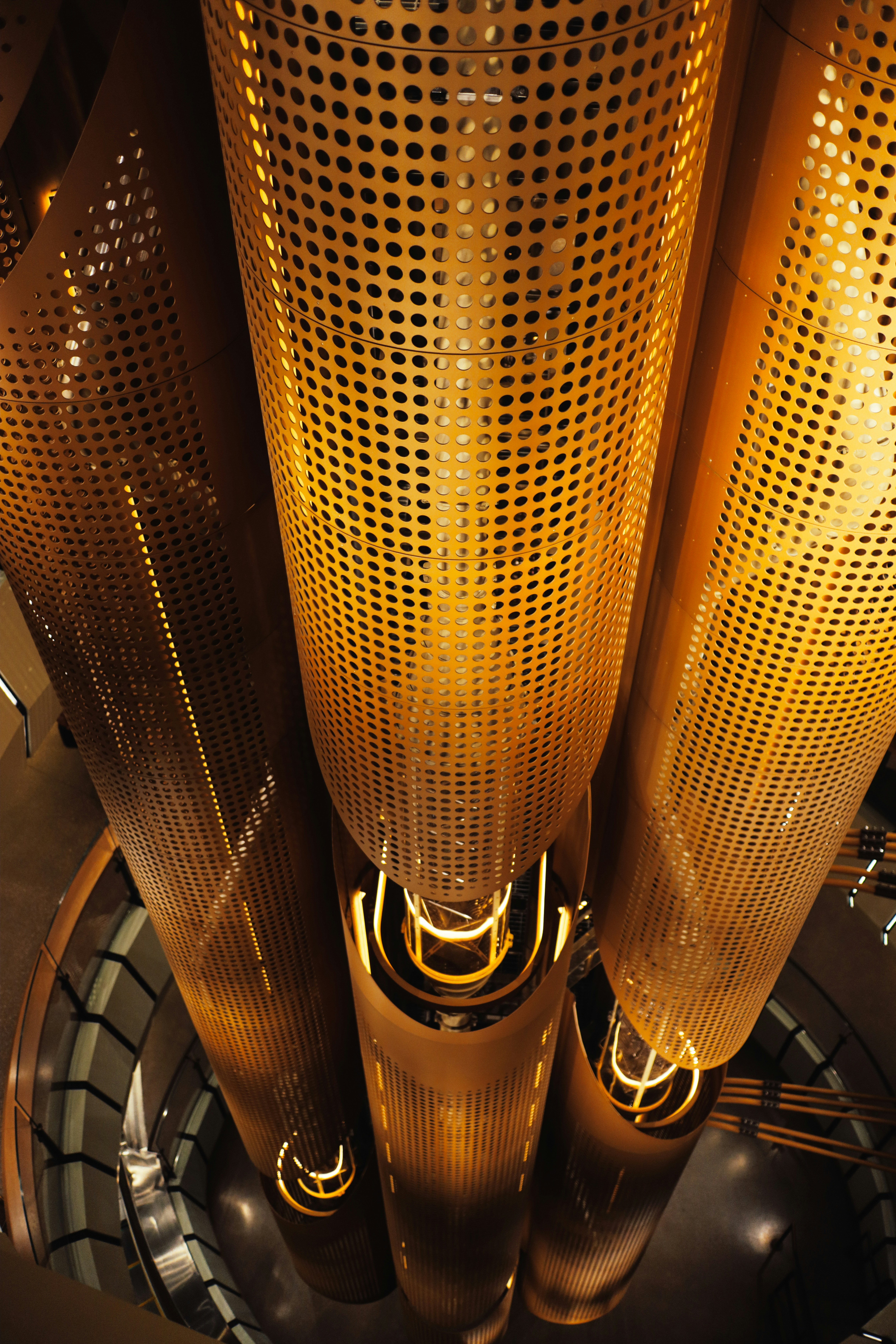 Golden, perforated cylindrical structures hang from ceiling. photo ...