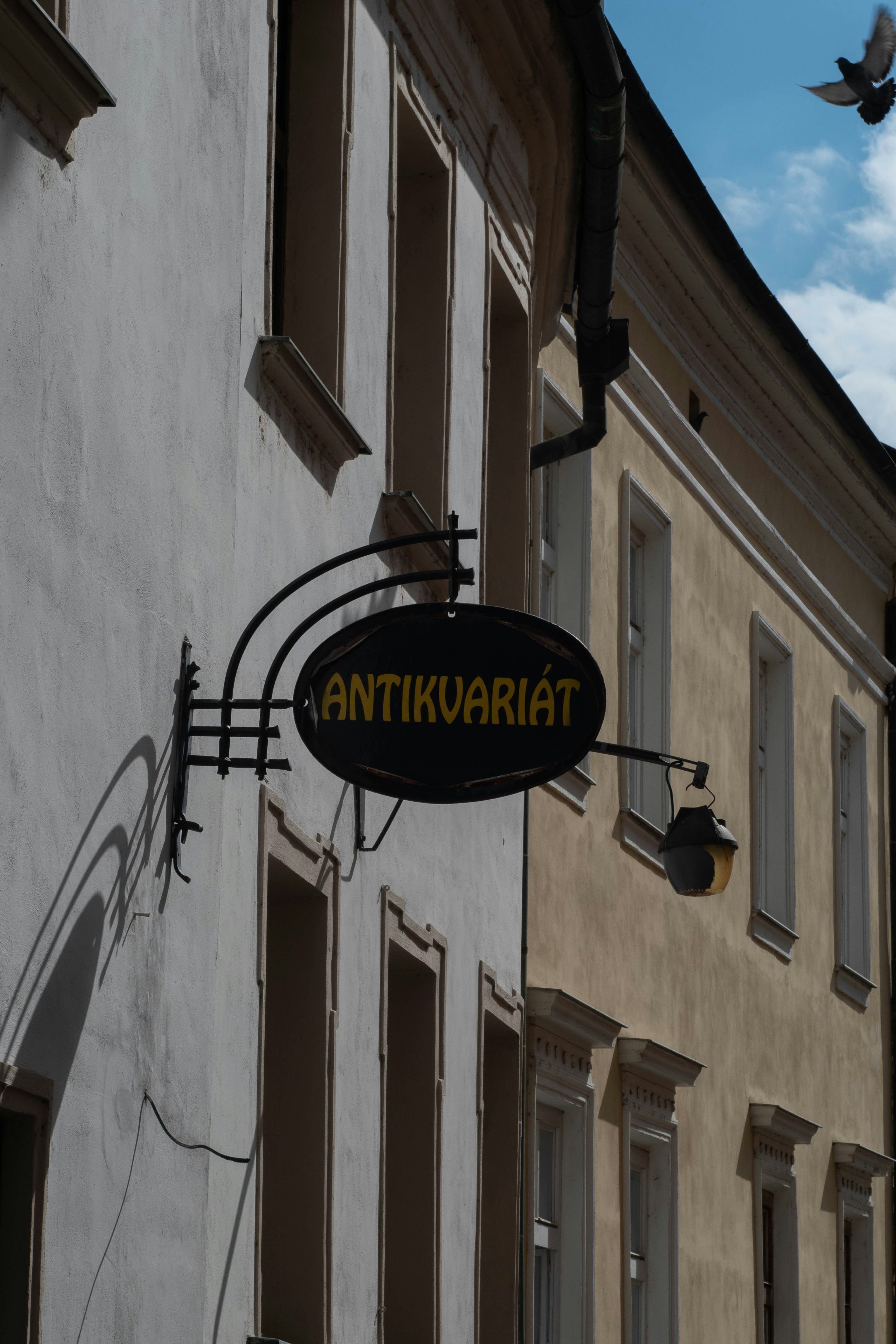 ANTIKVARIÁT on a sunlit European street: a vintage sign against pastel façades