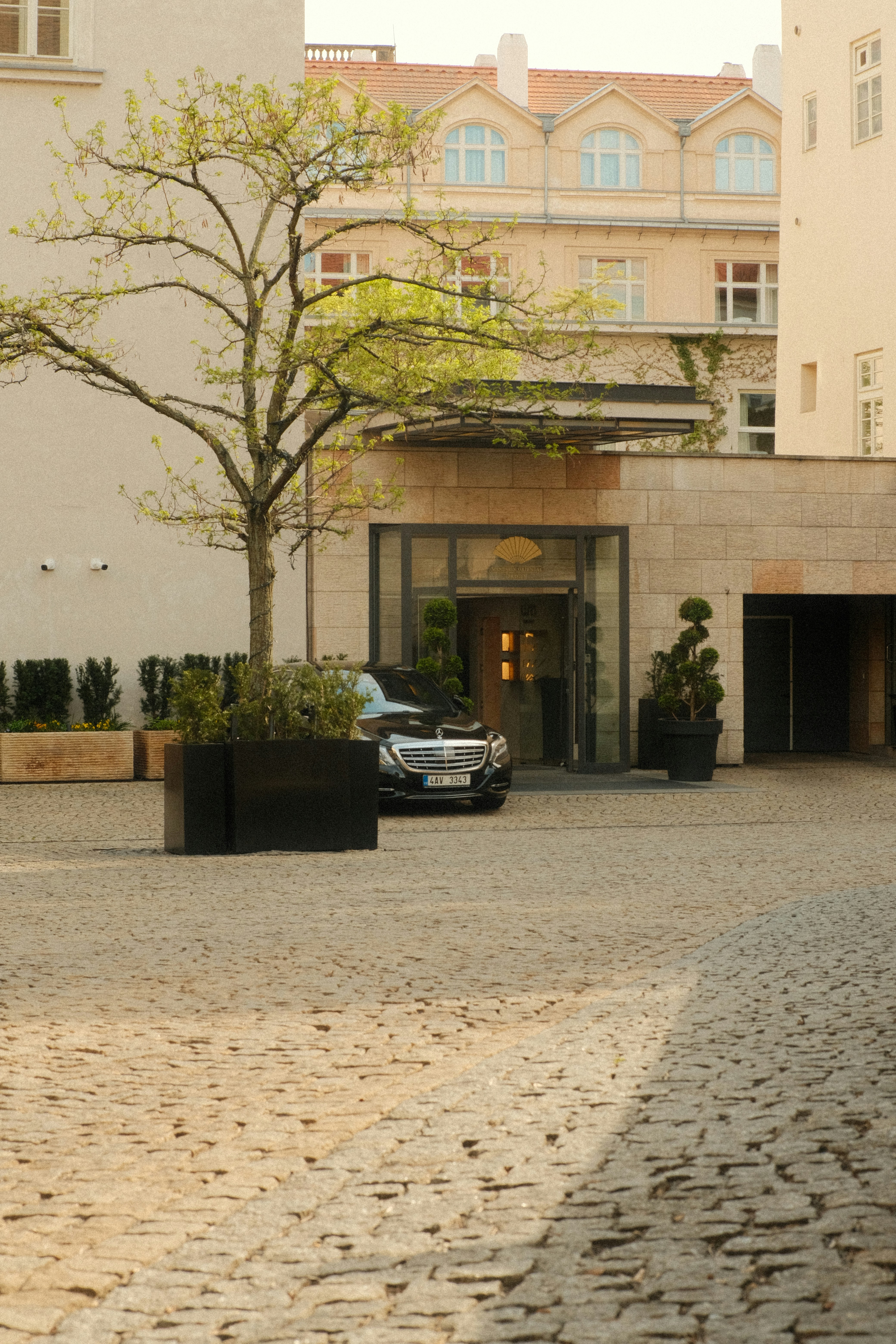 Sunlit Courtyard Arrival: A Sedan Framed by Planters and Glass Canopy