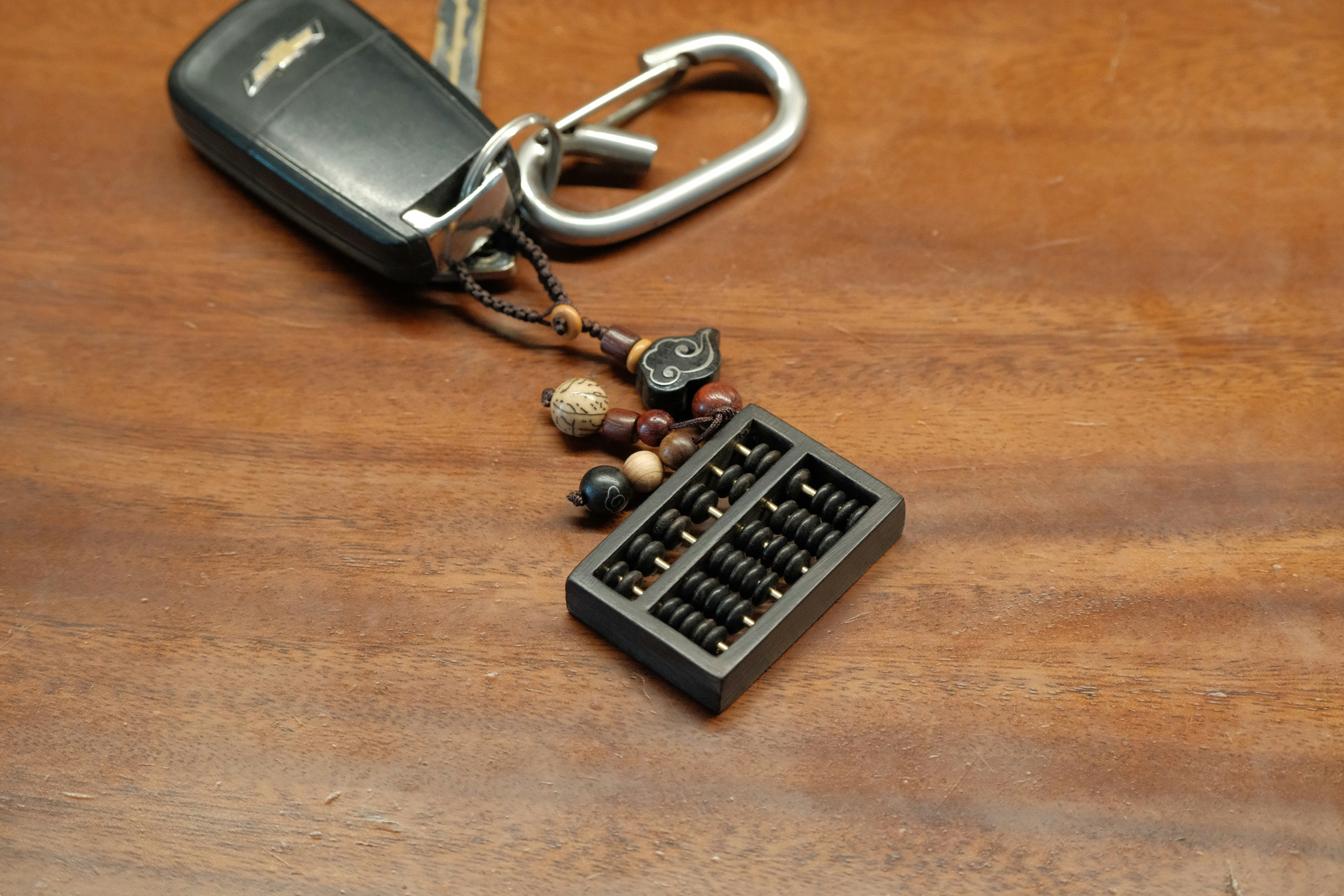 An intricately designed abacus keychain rests beside a car key on a wooden surface, blending classic craftsmanship with contemporary utility.