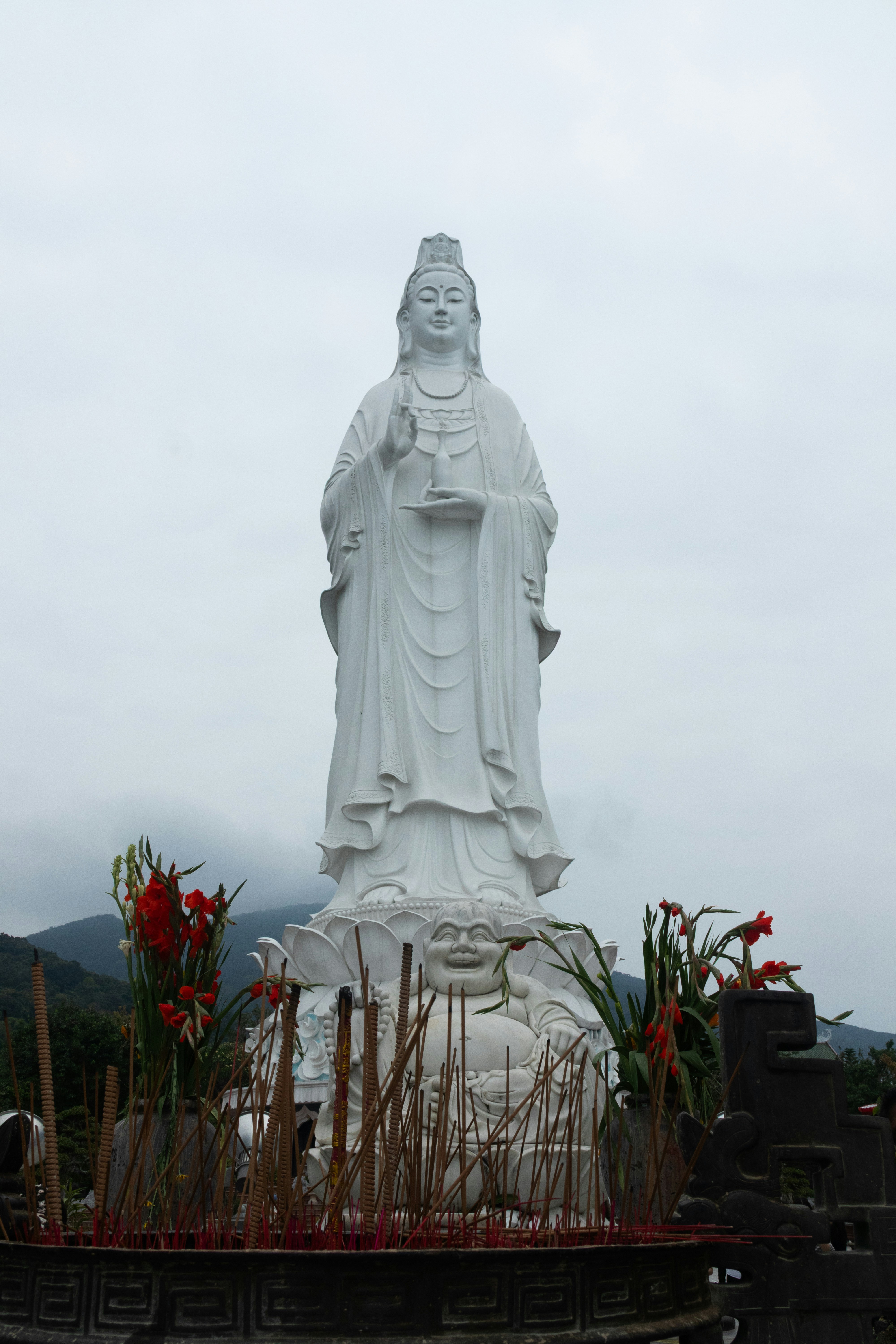 White Bodhisattva in Stone: A towering statue amid red offerings under a cloudy sky