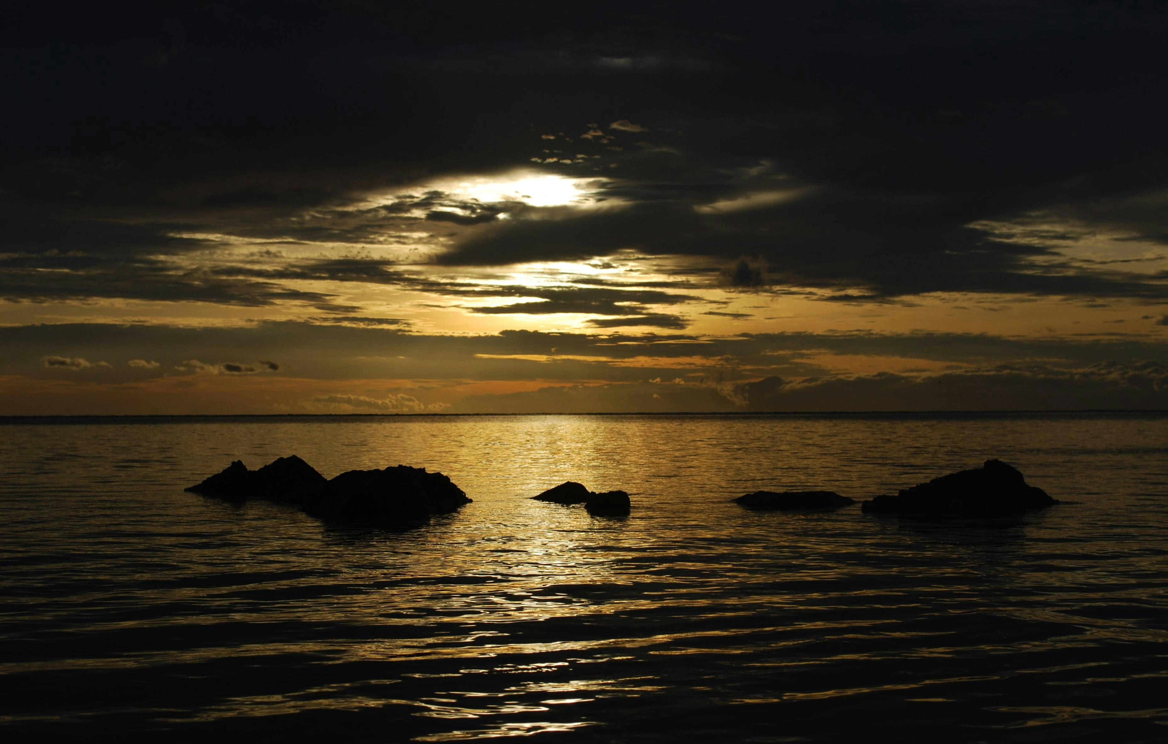 Sunset reflects on the water and the dark rocks. photo – Free Beach ...