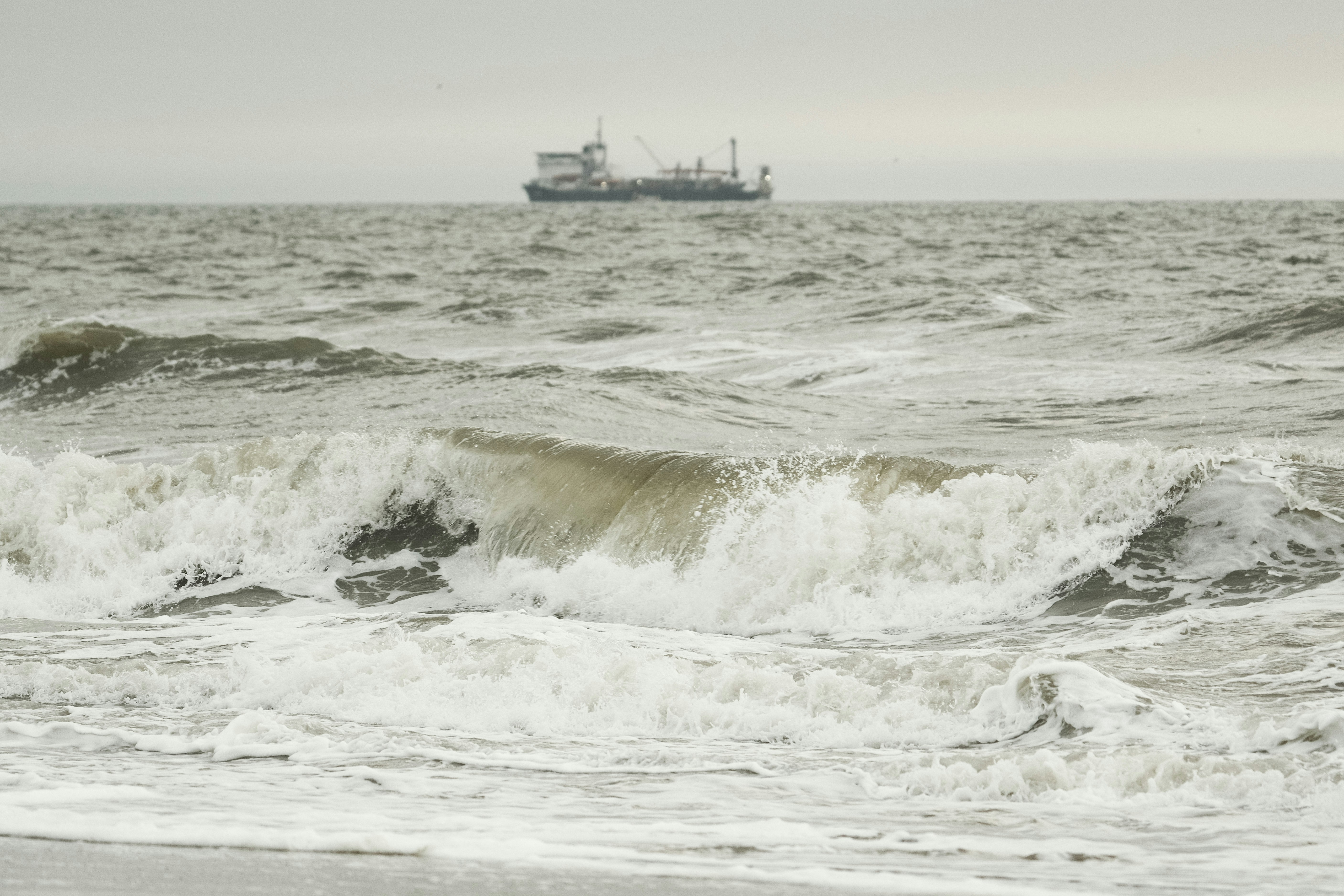 Las olas bravas rompen con un barco lejano a la vista. foto – Imagen de ...