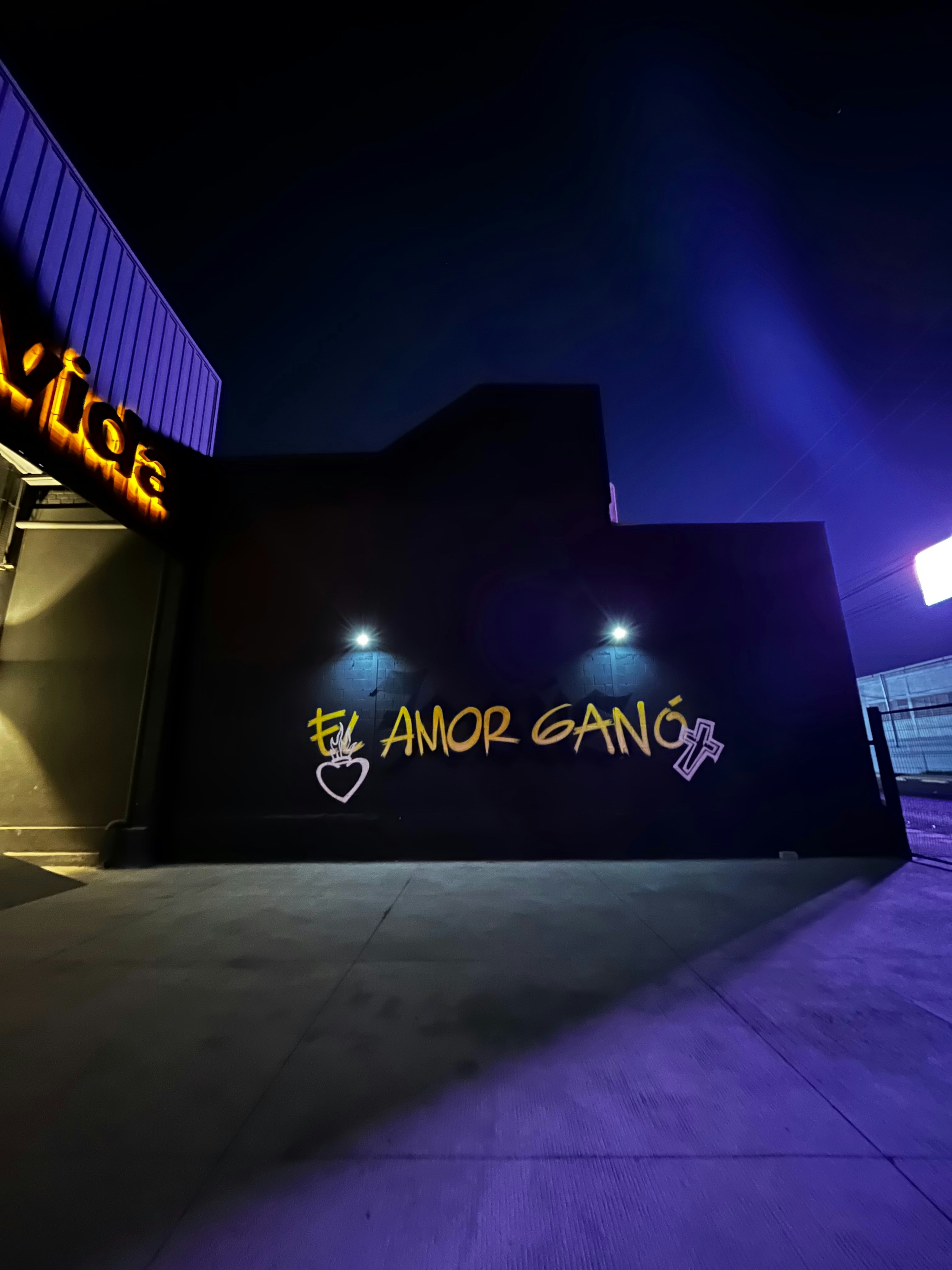 Vibrant graffiti reading 'El Amor Ganó' illuminated under streetlights on a dark wall, showcasing urban art culture.