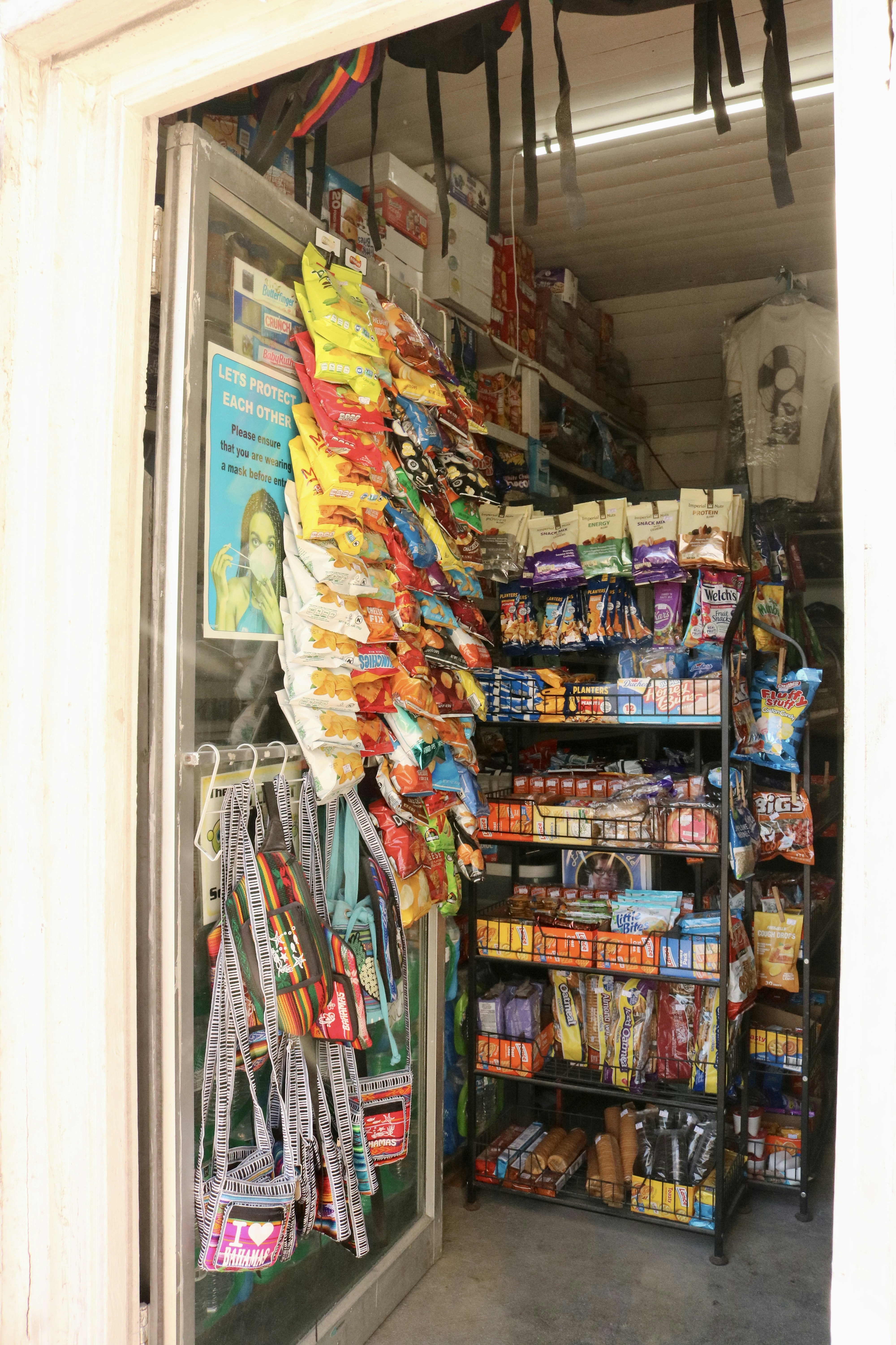 Vibrant display of snack foods and convenience items inside a small shop, inviting customers to explore. A poster advocating community health hangs prominently in the background.