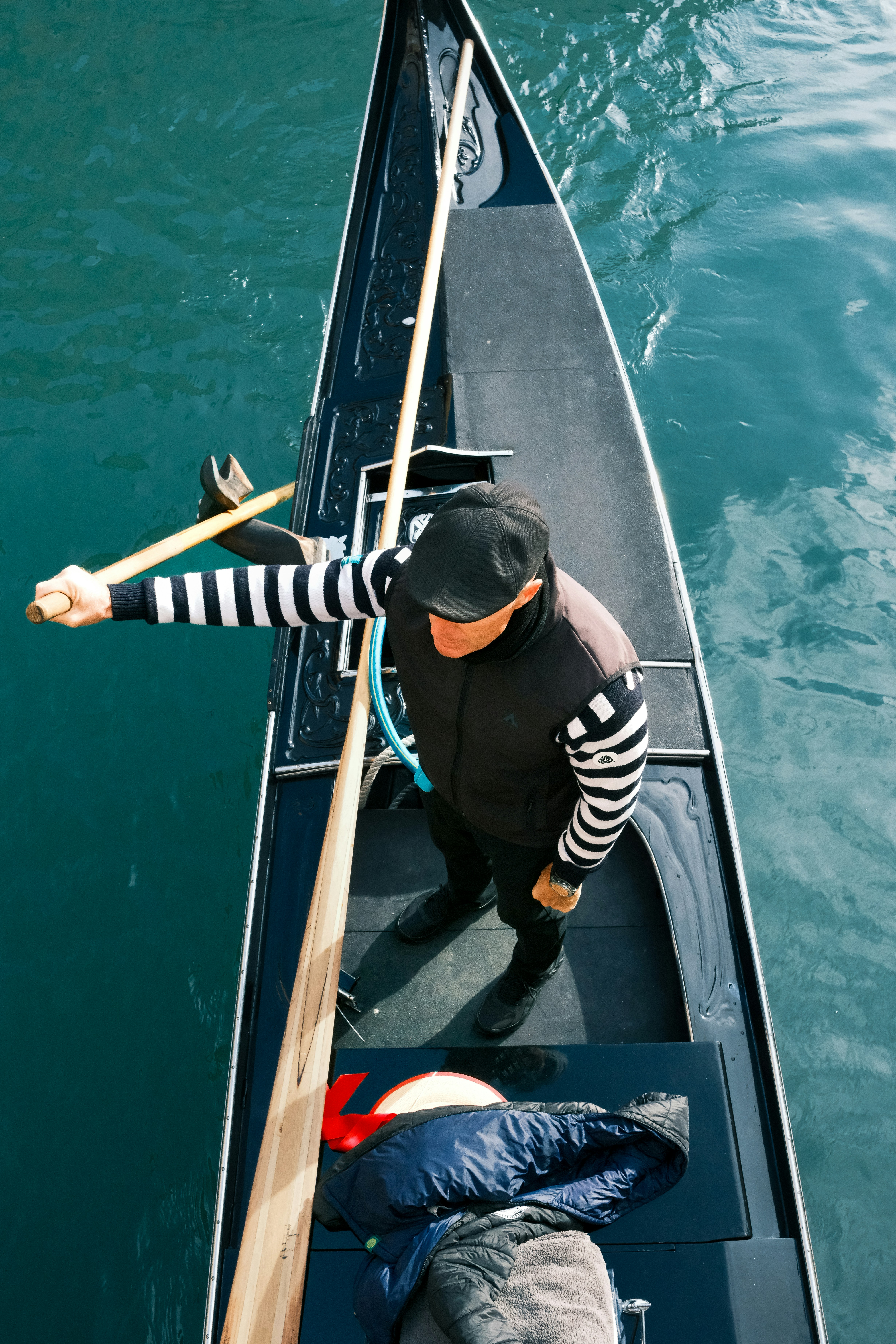 Emerald Glide: Striped-sleeve rower steering a narrow canal boat across turquoise water