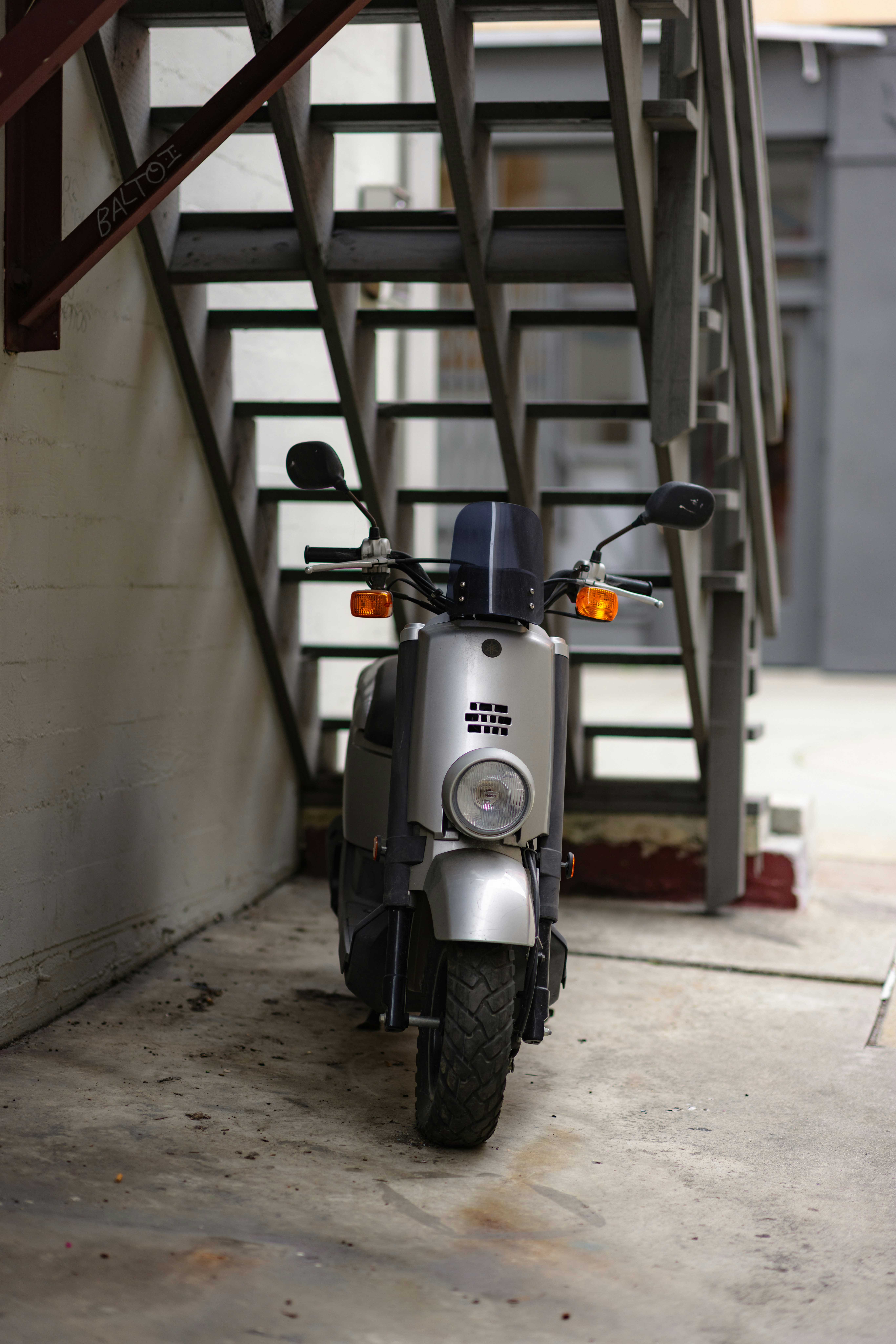 Under Steel Steps: A Silver Scooter Finds Focus in an Alley