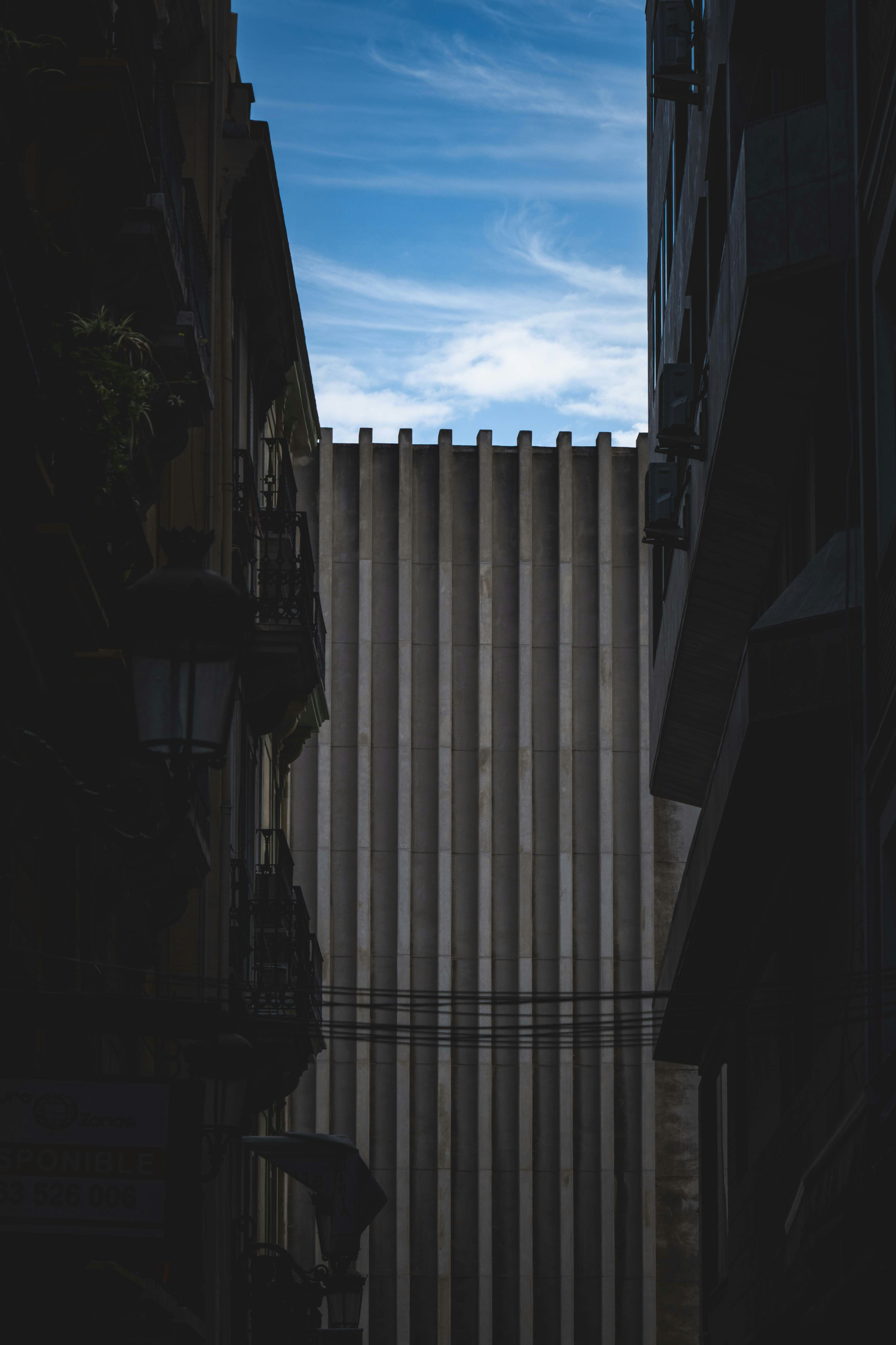 Tall, vertically striped building framed by narrow alleyways, with a clear blue sky peeking above. The contrast highlights the architectural lines.