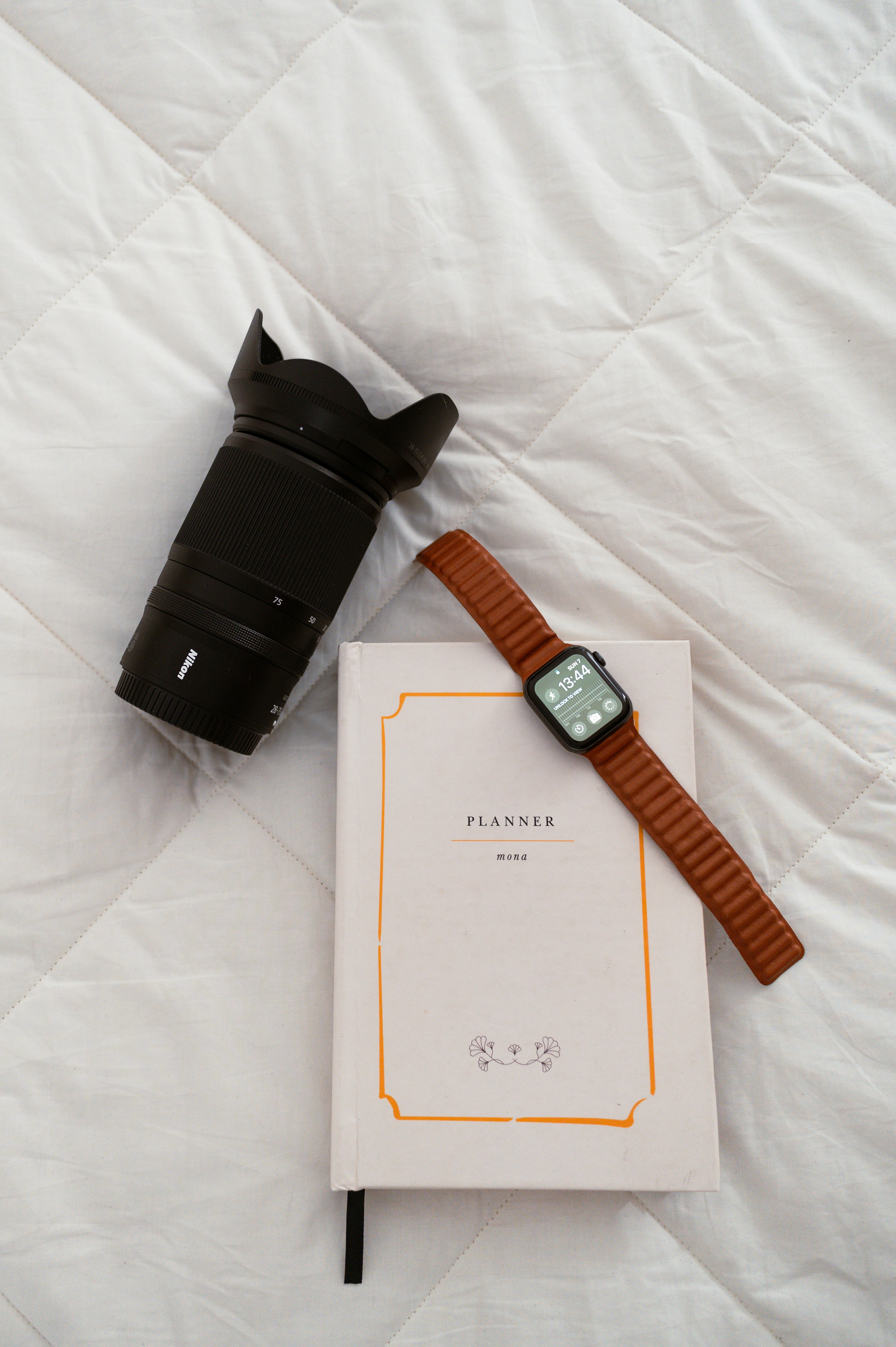 Camera lens, planner, and smartwatch arranged on a bed. photo – Free ...