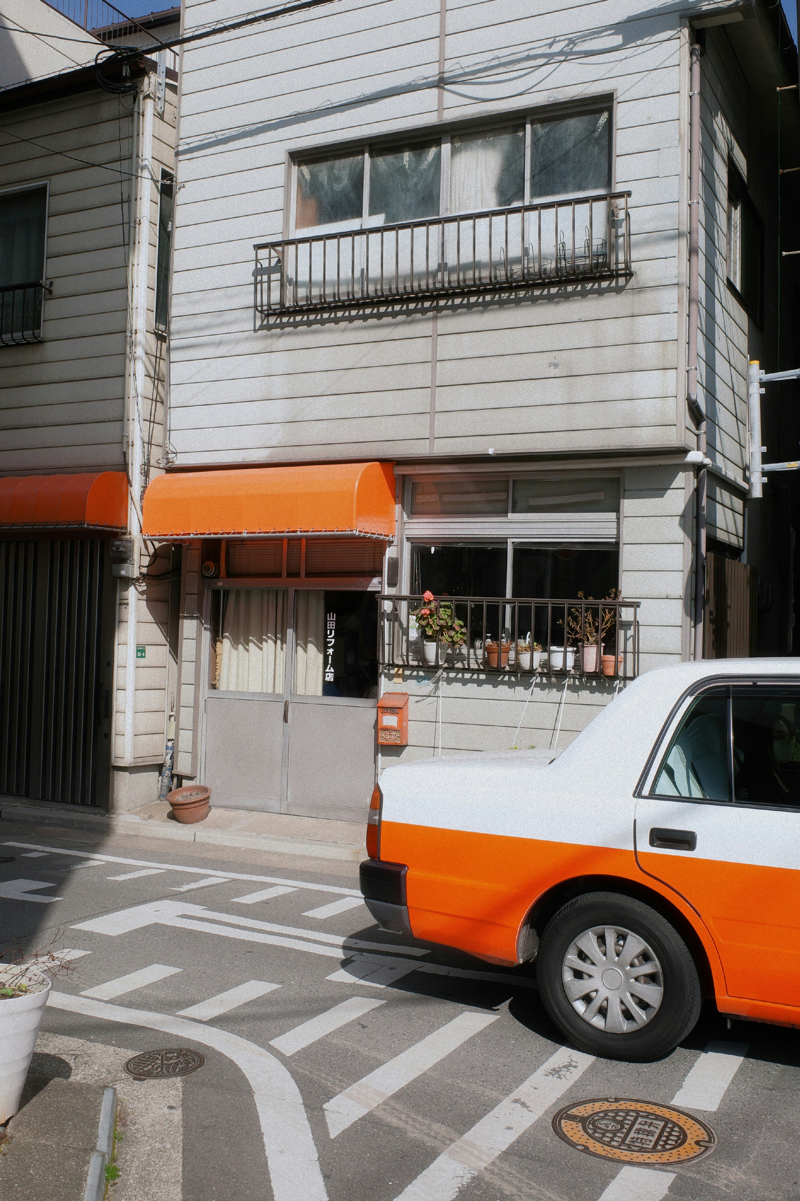 A vintage taxi parked in front of a quaint building adorned with orange awnings and potted plants, showcasing a slice of urban life.