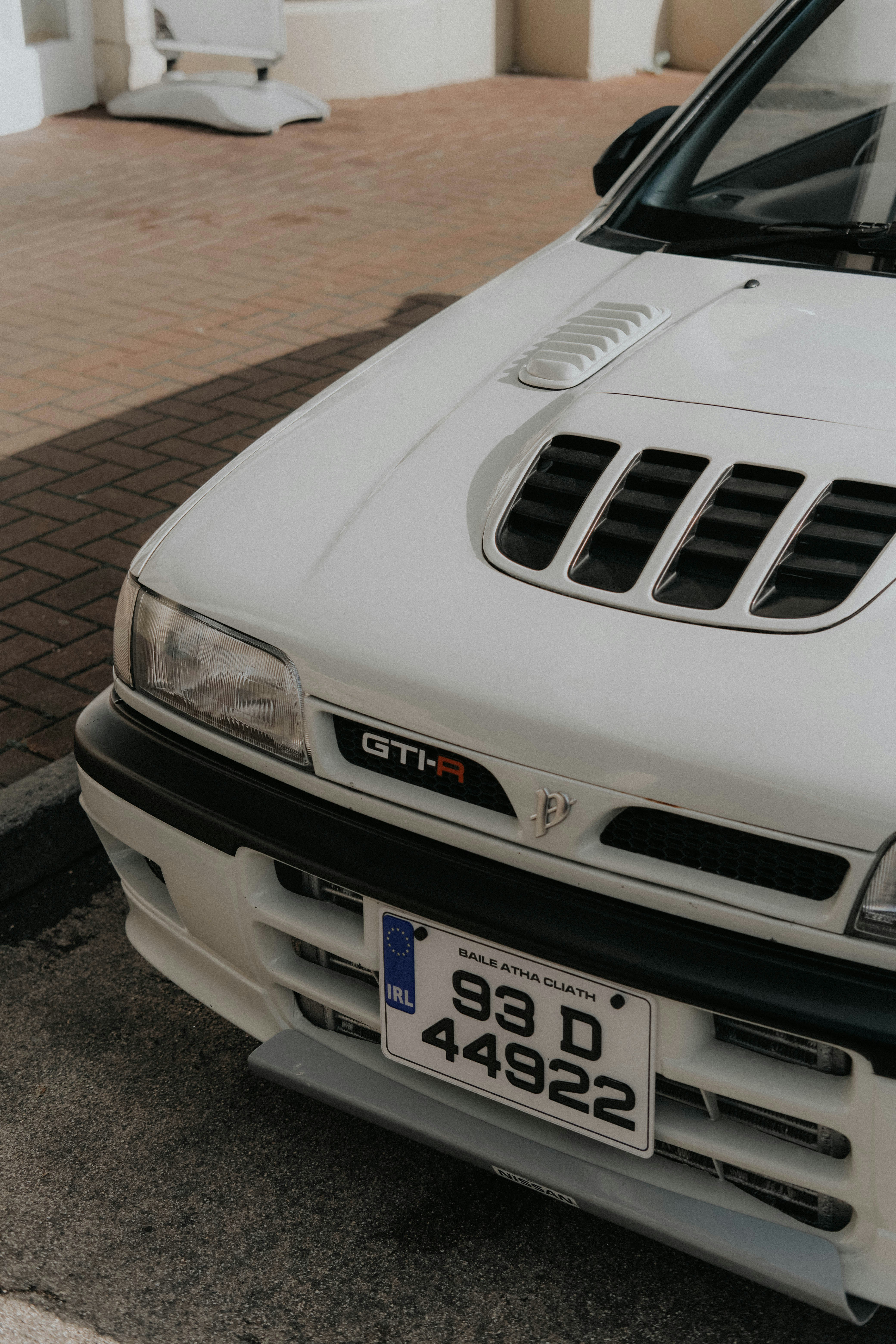 Close-up view of a white GTI-R showcasing its distinctive grille and hood vents, parked on a cobblestone street.