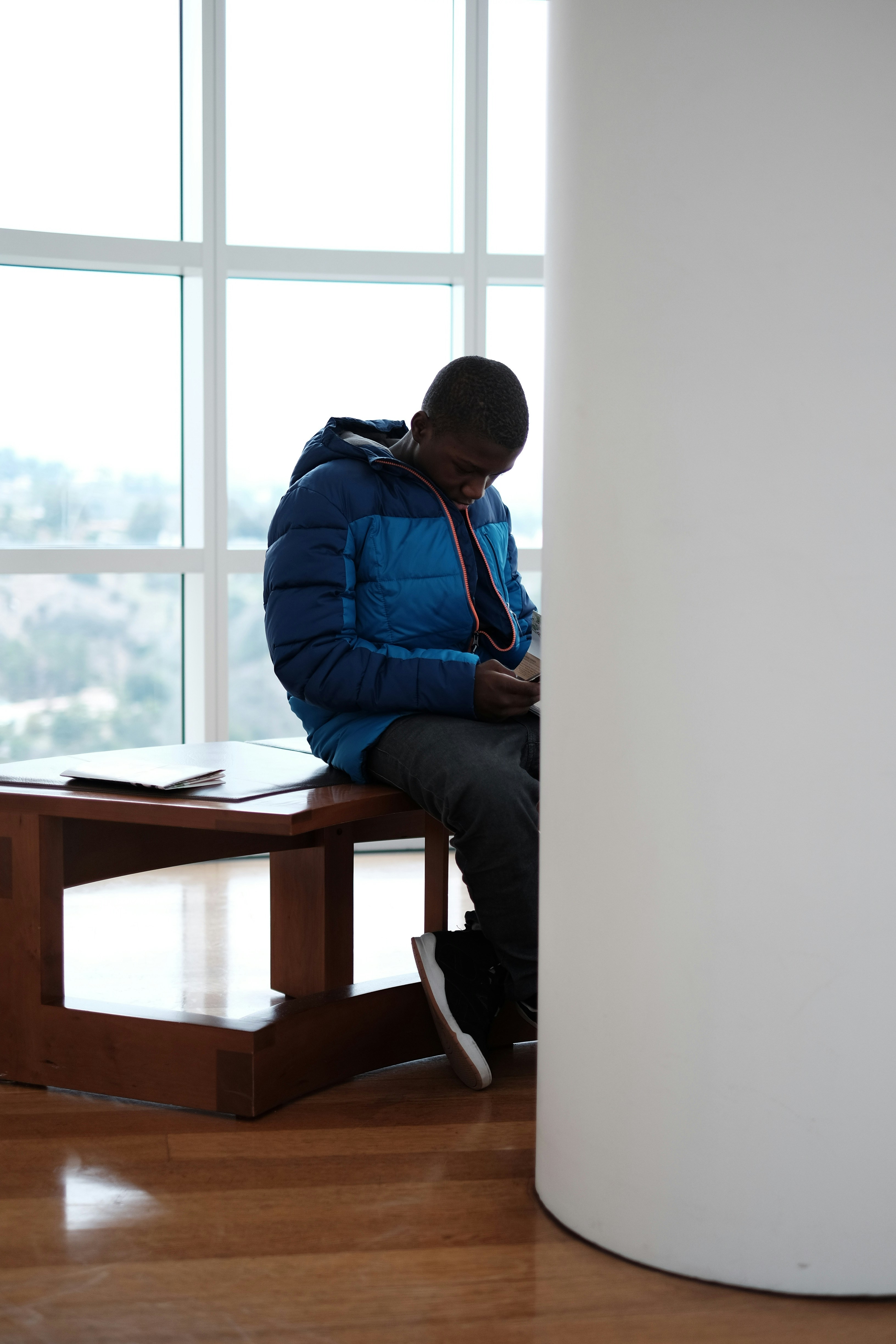Blue Stillness by the Window: A Lone Sitter in a Puffer Jacket