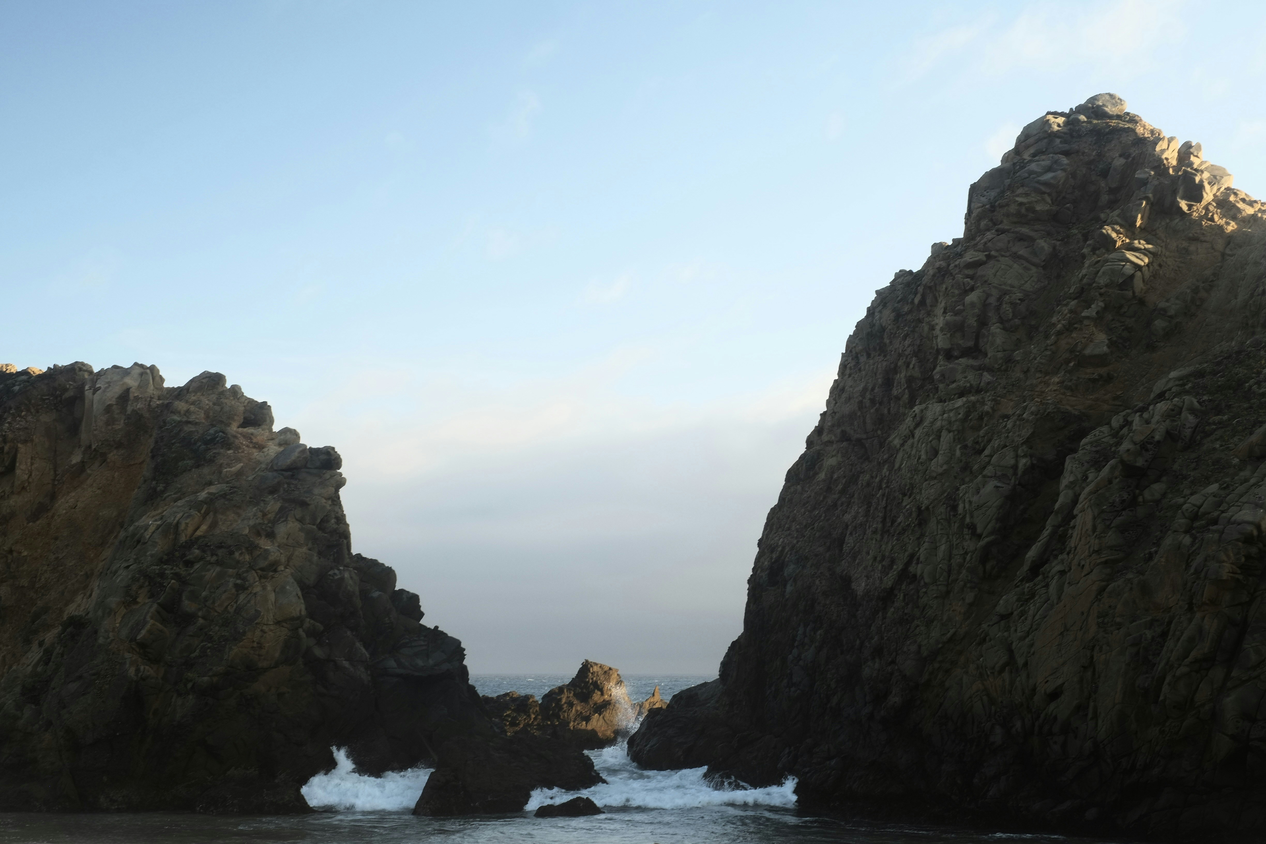 Jagged cliffs frame the ocean under a light blue sky. photo – Free ...