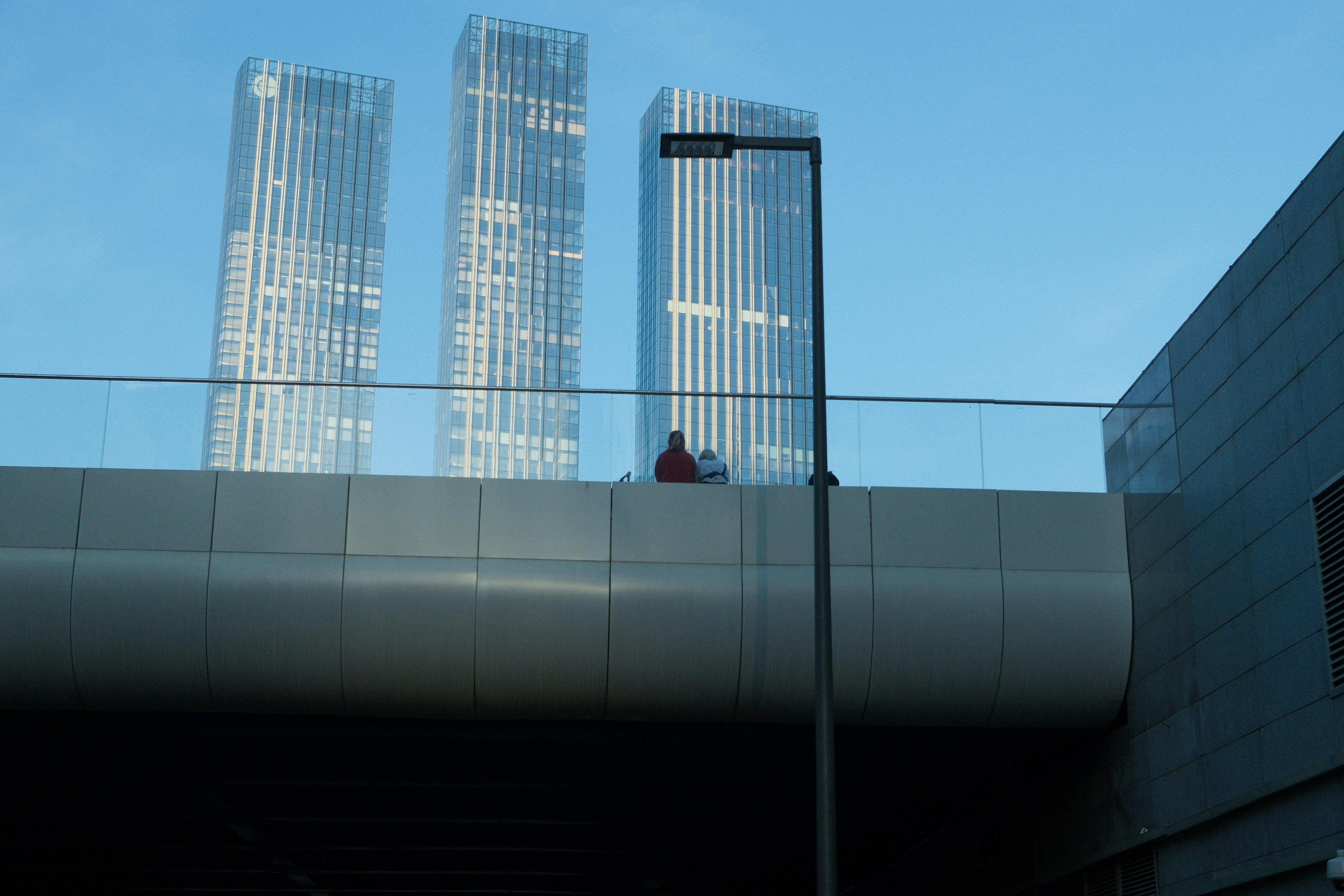 Red-Jacket Sentinel on a Glass Bridge Beneath Twin Glass Towers