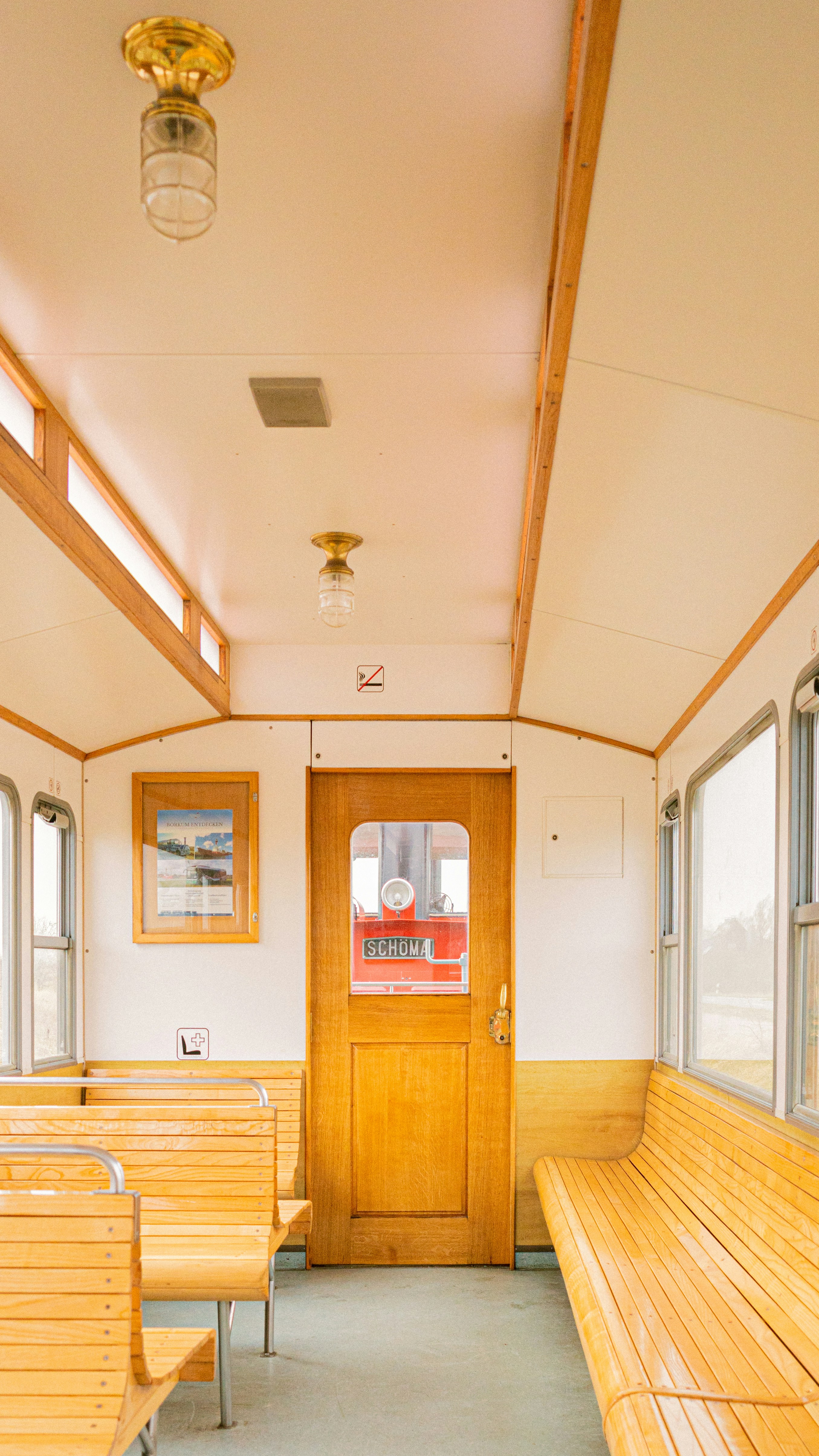 Interior of a vintage train carriage featuring wooden benches and a classic door with a window. Warm lighting enhances the nostalgic atmosphere.