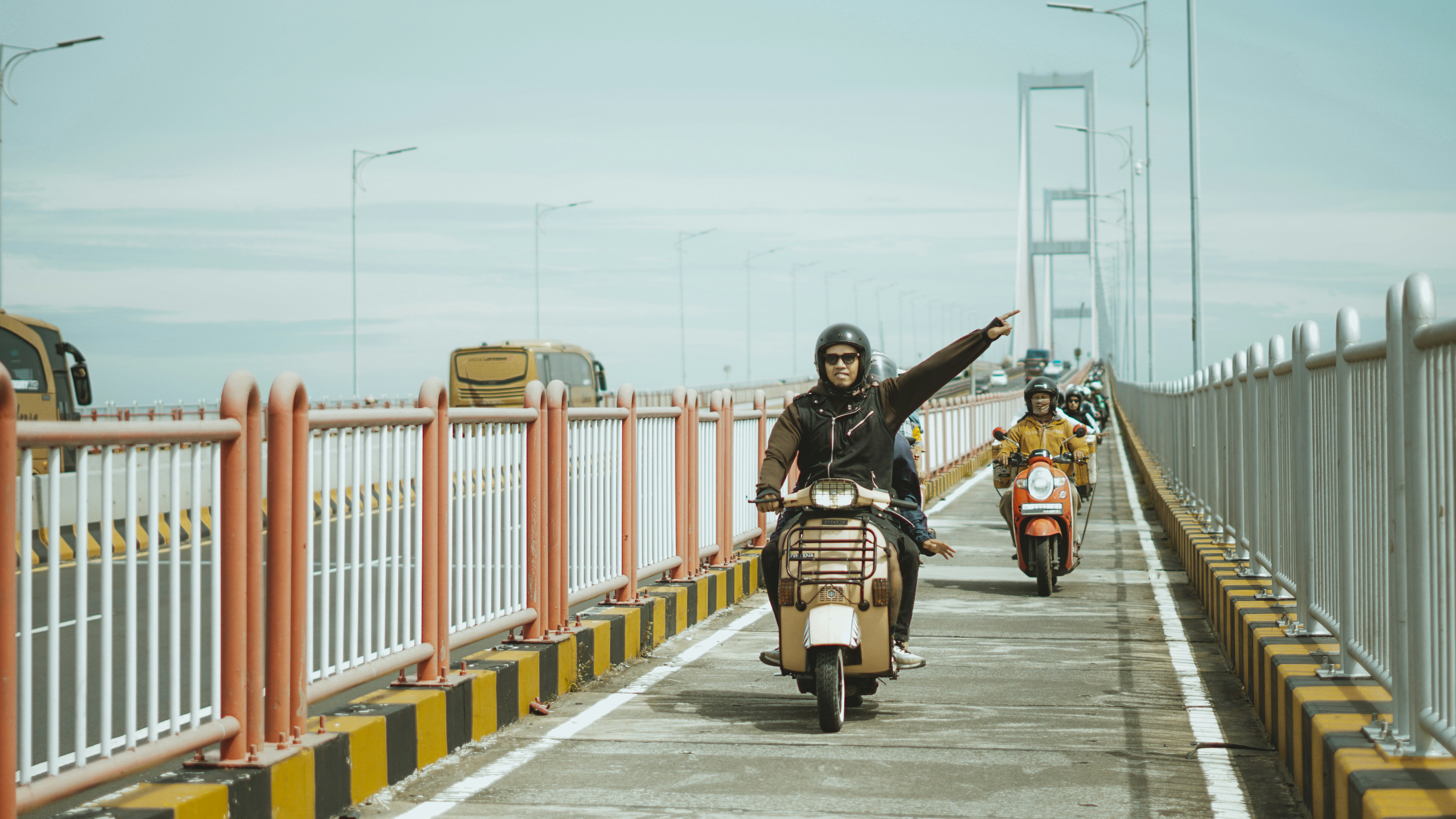 Lead Rider Waves Across a Sunlit Bridge: A Scooter Parade in Motion