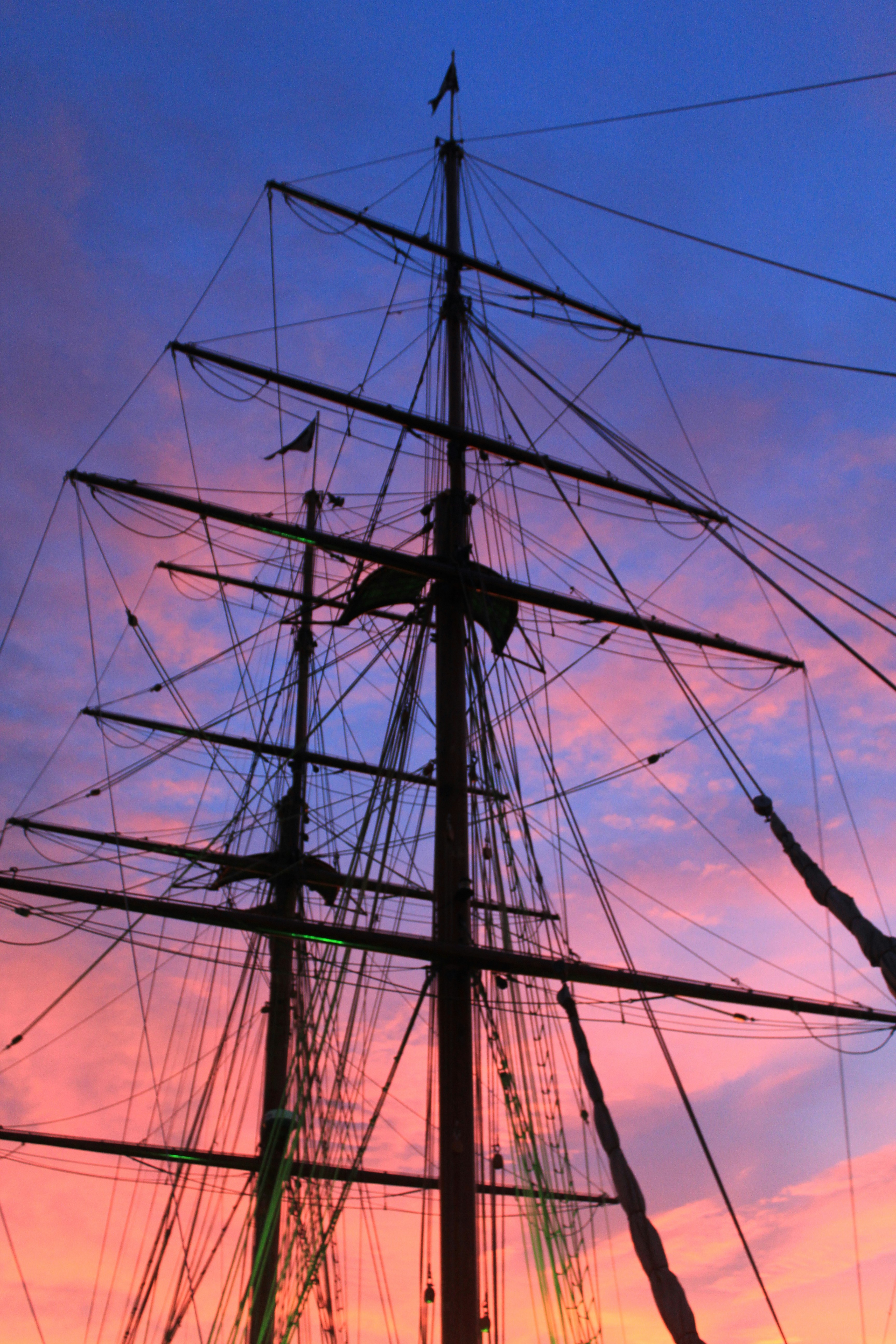 Silhouette of a tall ship's mast and rigging against a vibrant sunset sky filled with hues of pink and blue.